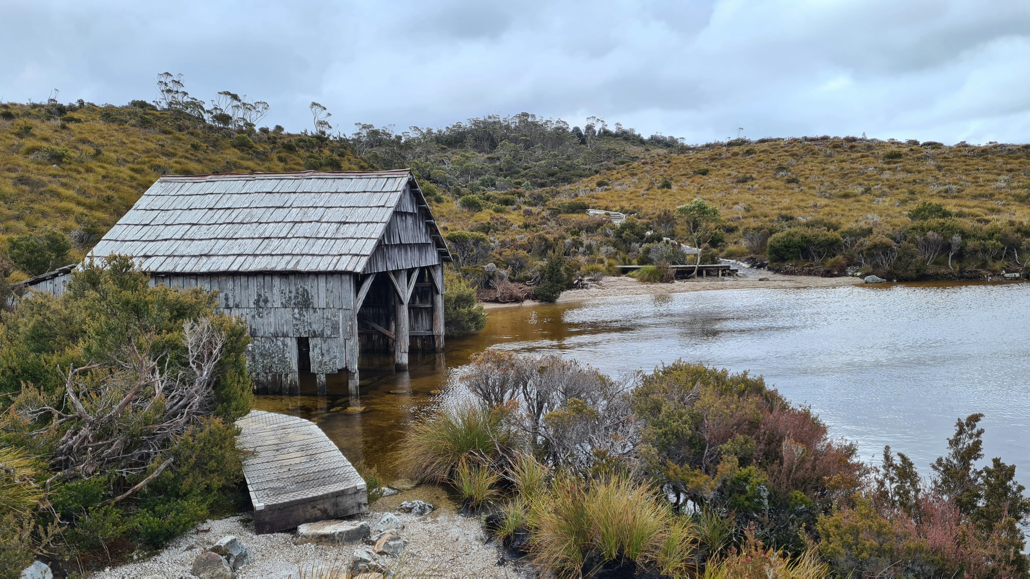 Weathered boathouse reflecting in tranquil water, surrounded by lush greenery and rolling hills. A serene landscape capturing the essence of nature's harmony.