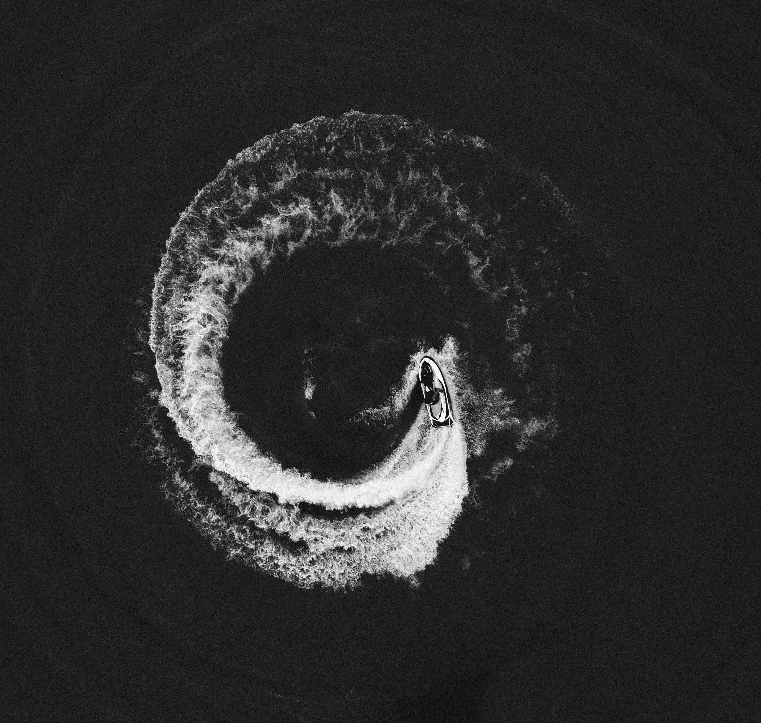 A speedboat carves a dynamic spiral through the water, creating a striking contrast against the dark surface. The motion captures the essence of thrill and adventure.