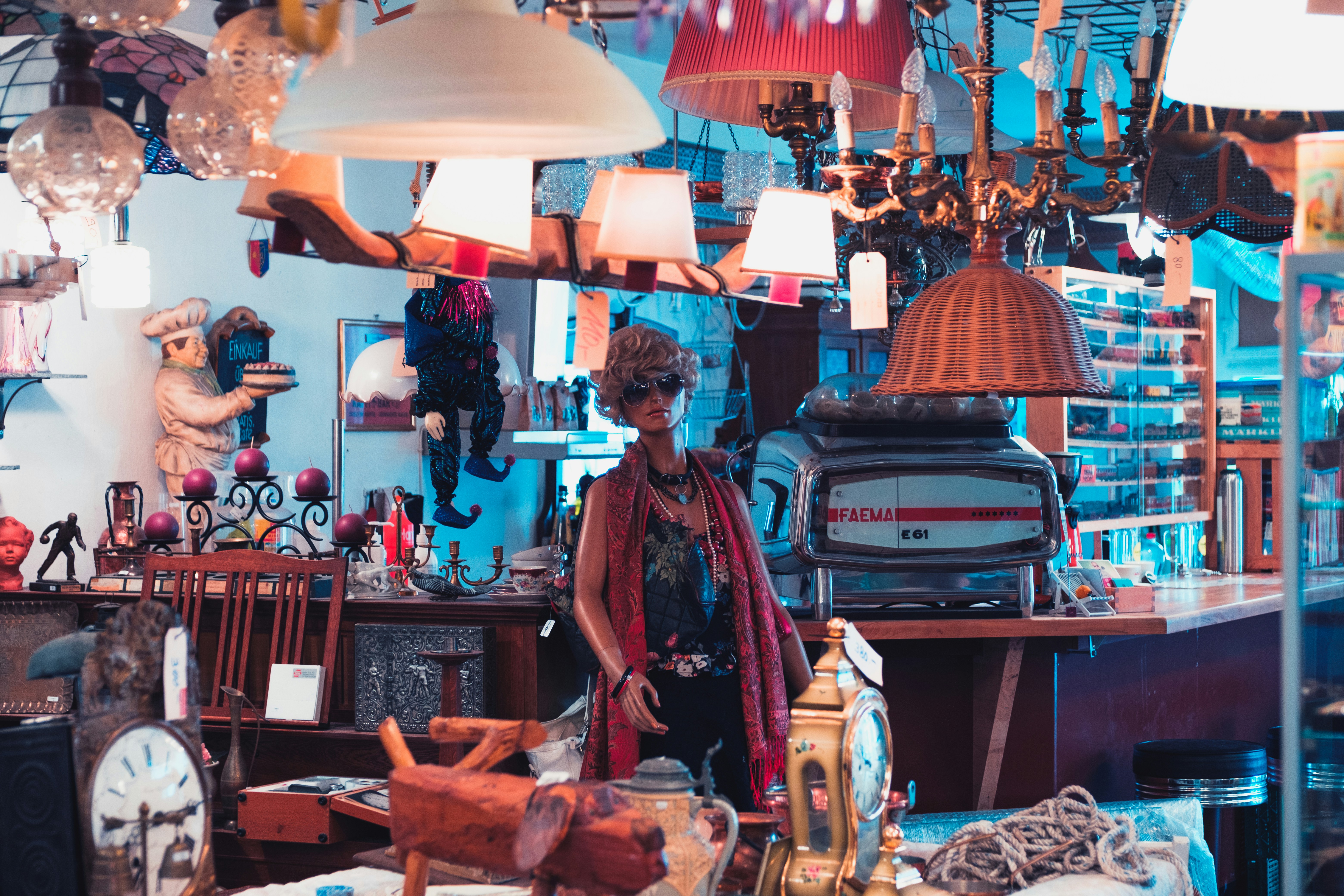 A vintage shop filled with eclectic items, featuring a mannequin dressed in vibrant clothing amidst an array of antique decorations and warm lighting.