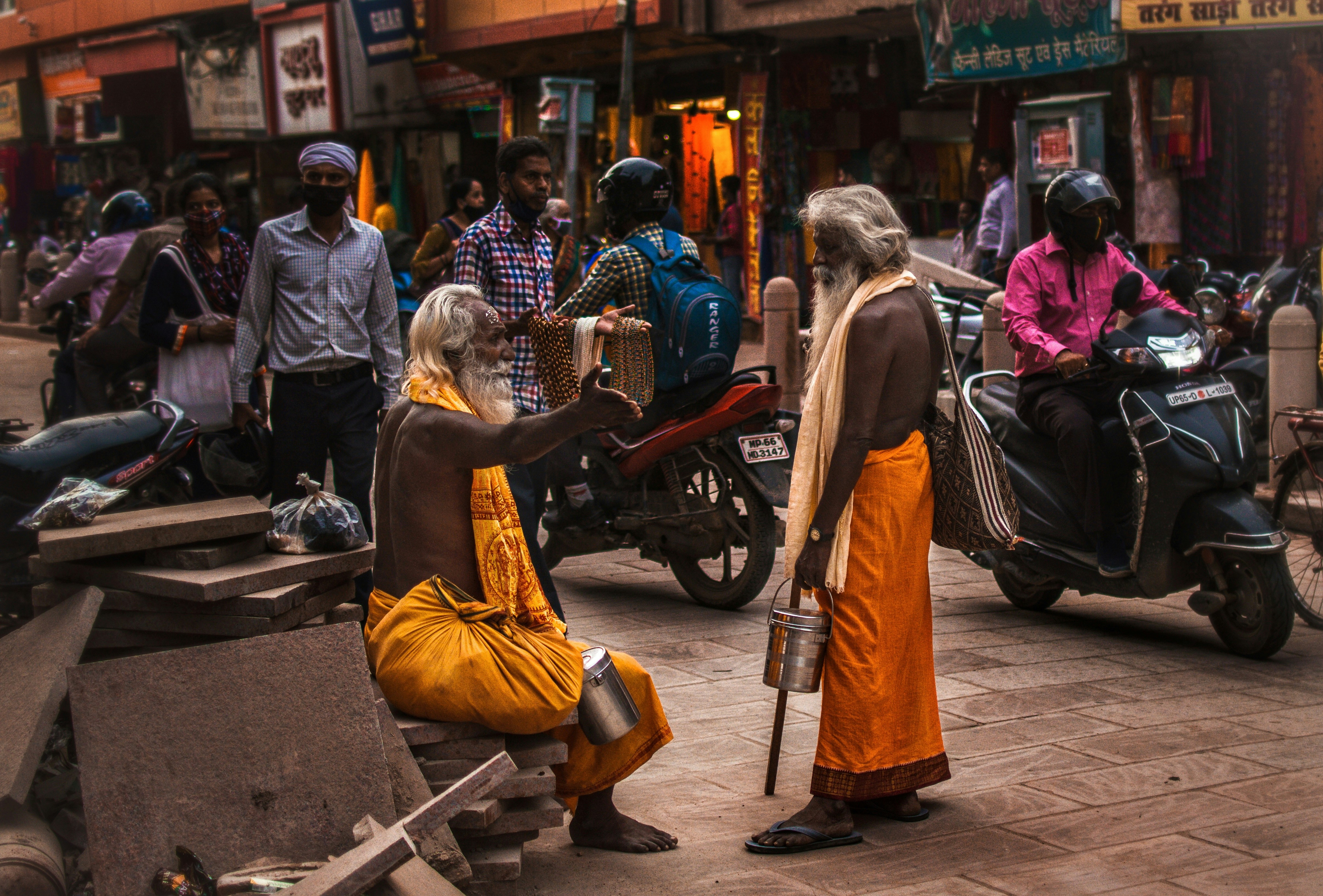 Two sadhus engage in discussion on a bustling street in Varanasi, surrounded by pedestrians and scooters.