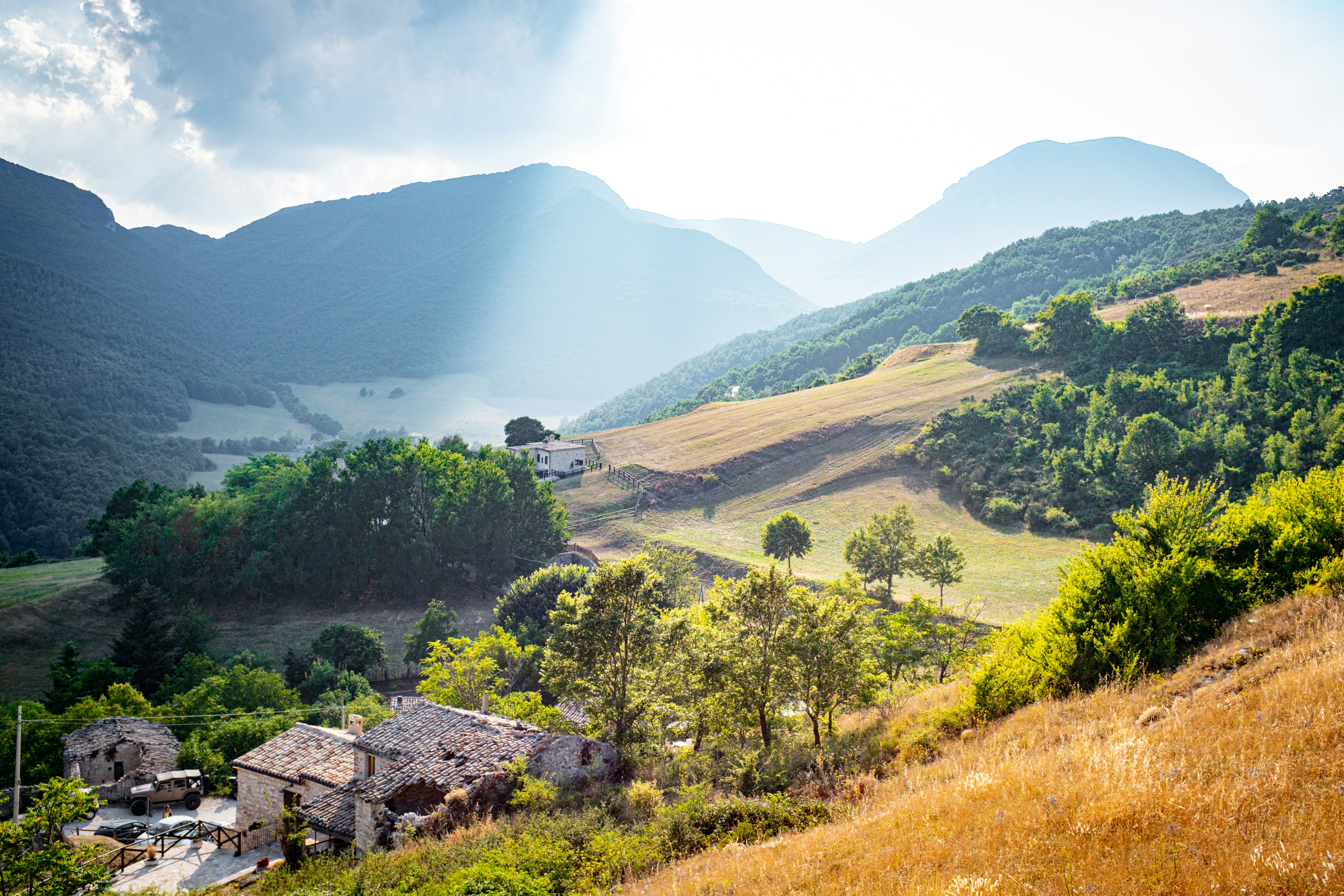 Rolling hills and valleys with sunlight streaming through mountain peaks in the distance.