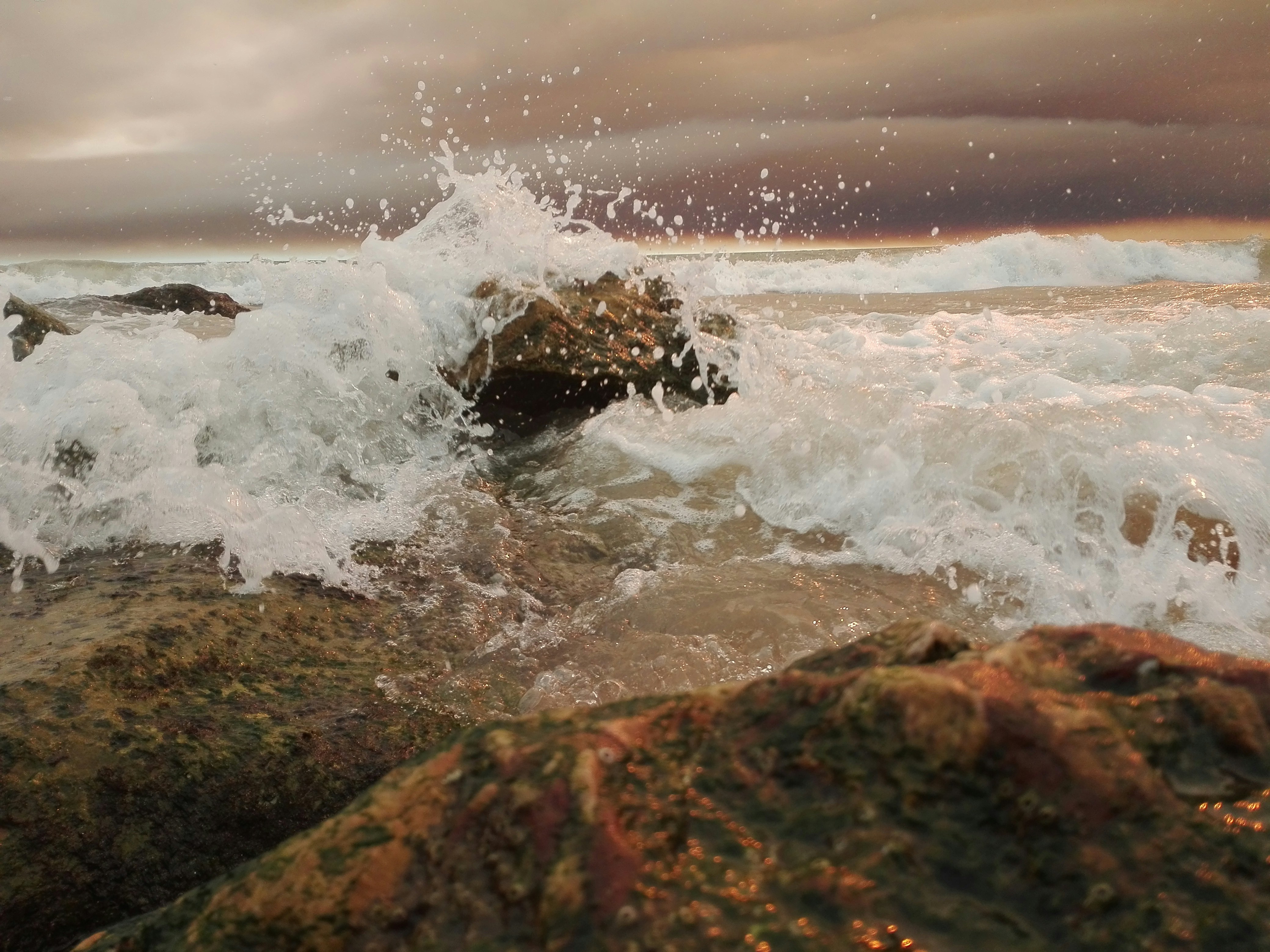 Waves crashing against rugged rocks at twilight, capturing the dynamic interplay between land and sea.