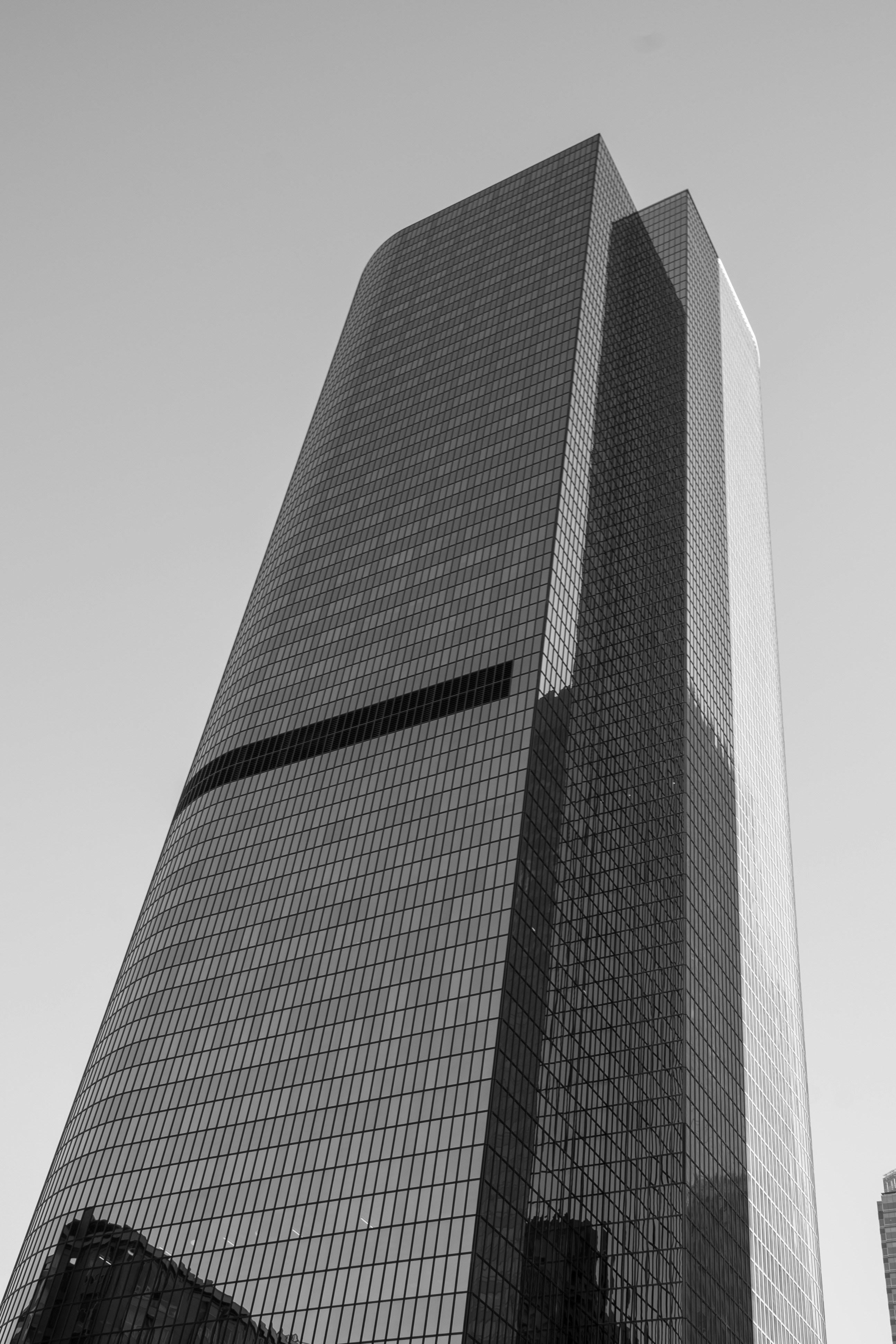 A dramatic view of a sleek skyscraper, showcasing its reflective glass facade against a clear sky. The upward perspective emphasizes the building's towering presence.