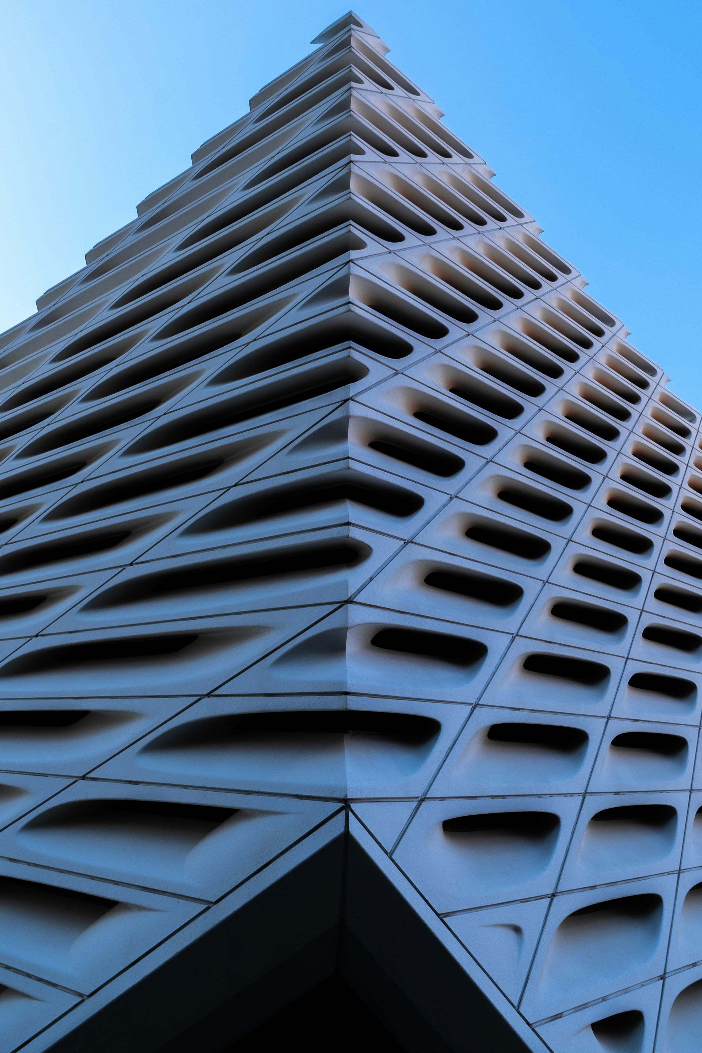 Close-up of a modern building's textured facade, showcasing a unique pattern of cutouts and geometric lines against a clear blue sky.