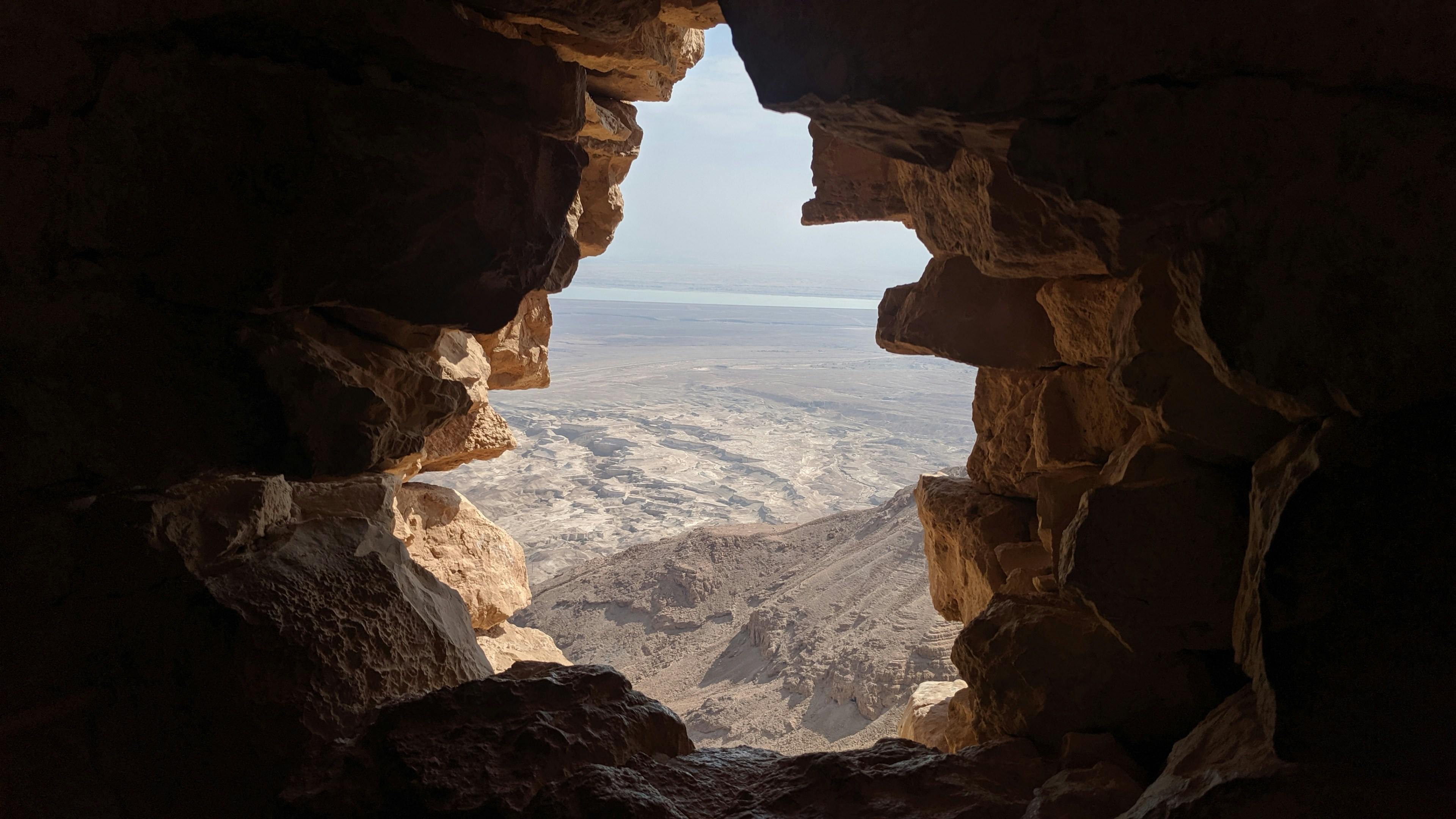 View through a rocky opening showcasing a vast desert landscape under a clear sky.