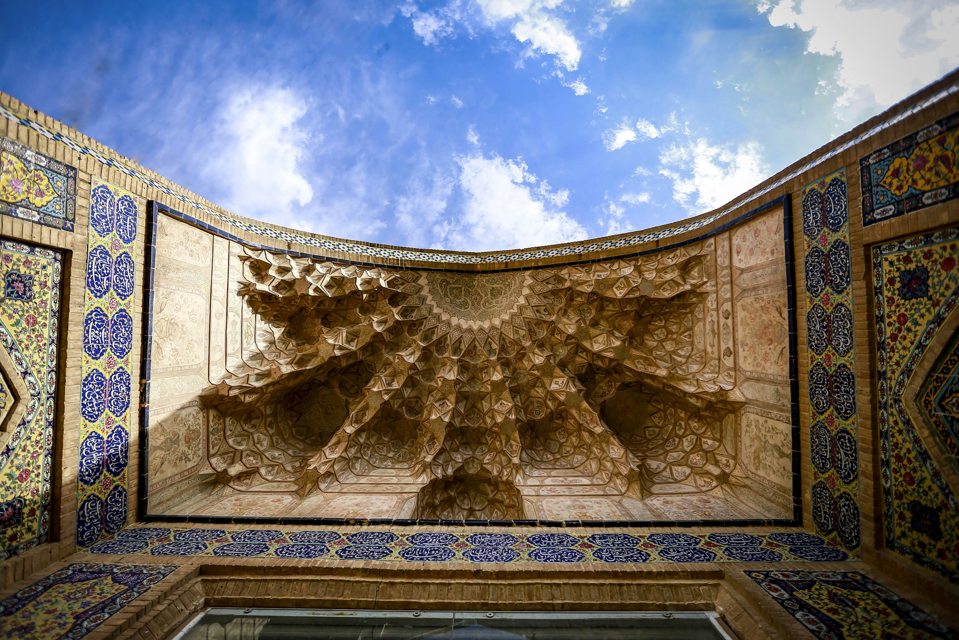 Intricate ceiling design showcasing detailed craftsmanship and vibrant tile work beneath a bright blue sky.