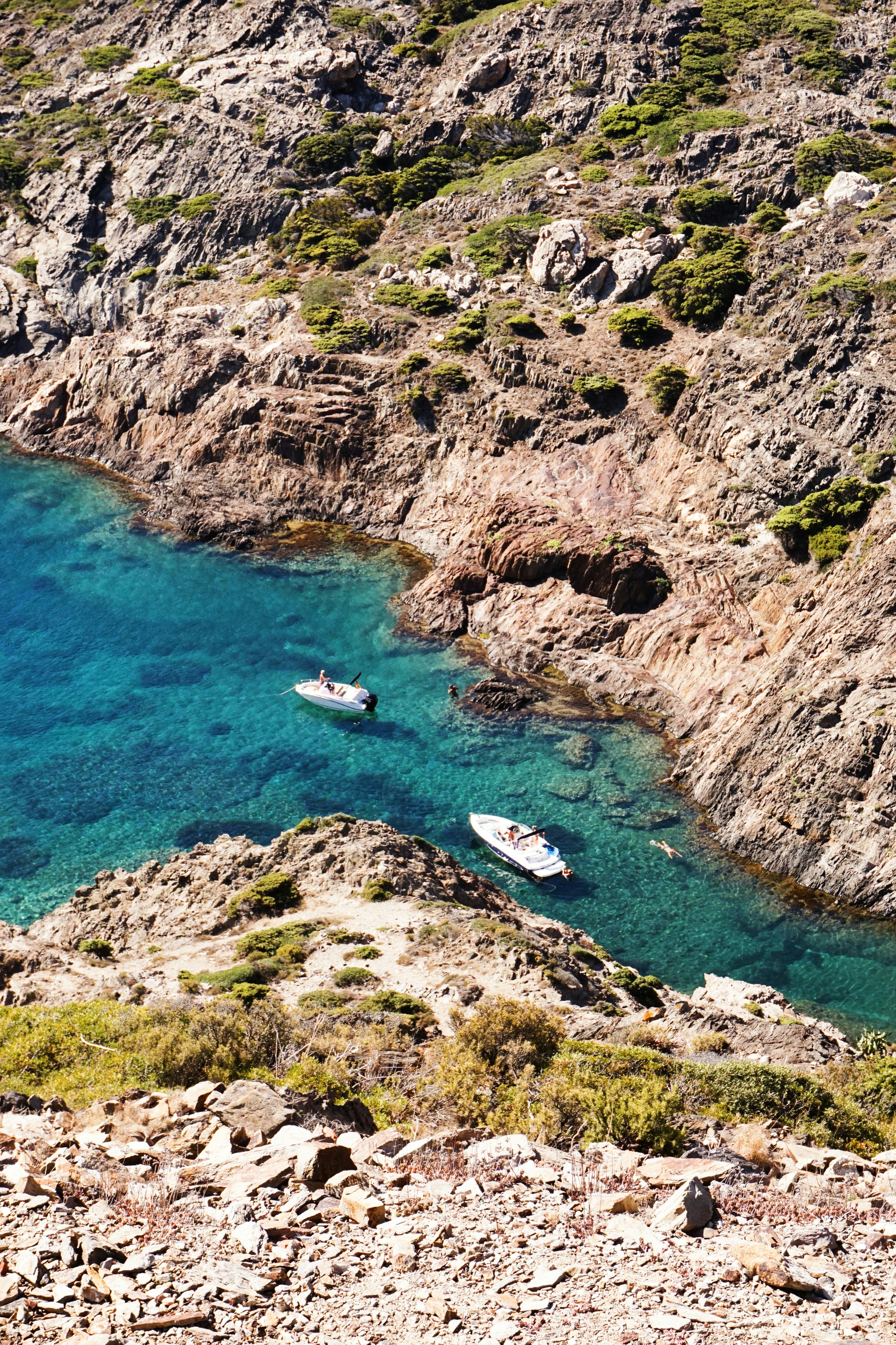 White boats anchored in a clear turquoise cove surrounded by rocky cliffs and sparse greenery.