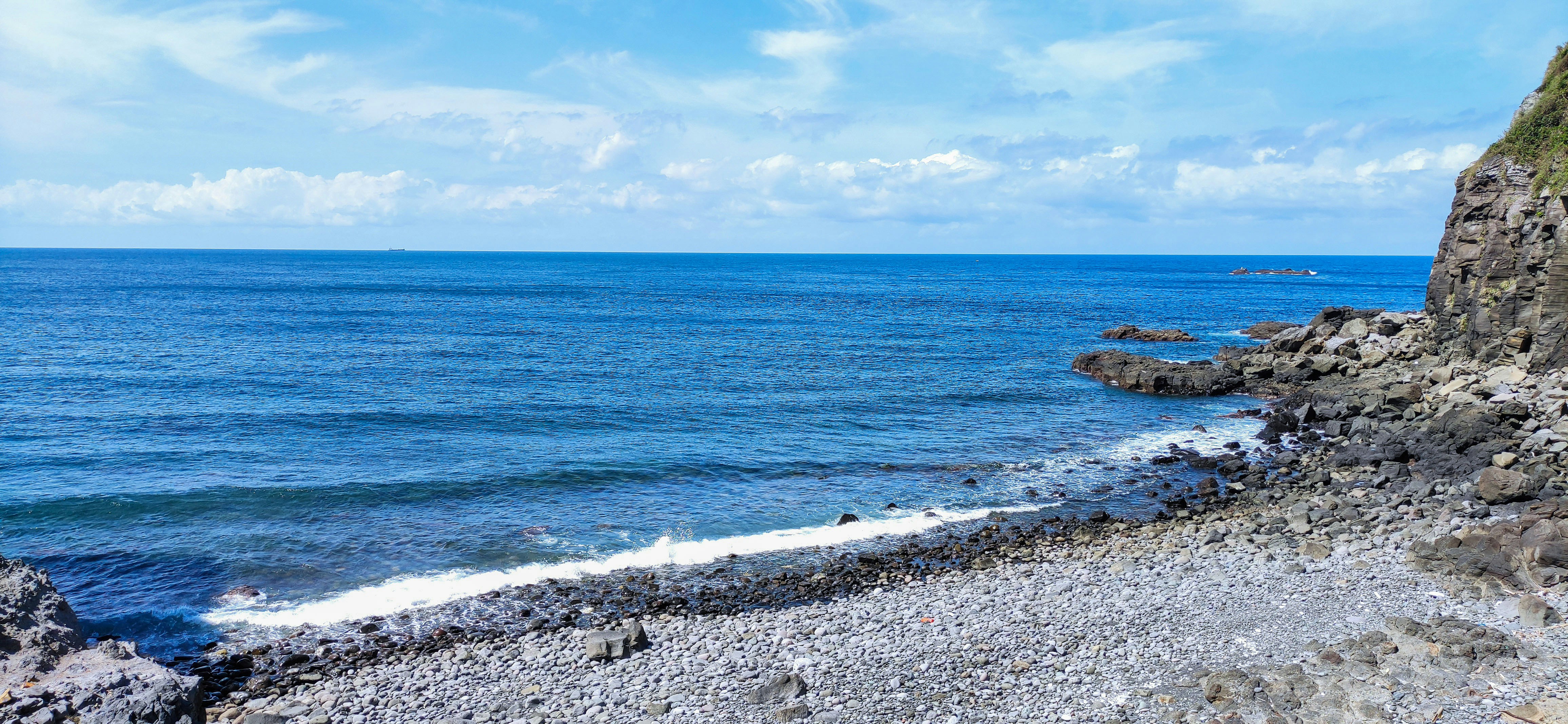 Rocky shoreline meeting a tranquil blue ocean under a vibrant sky.
