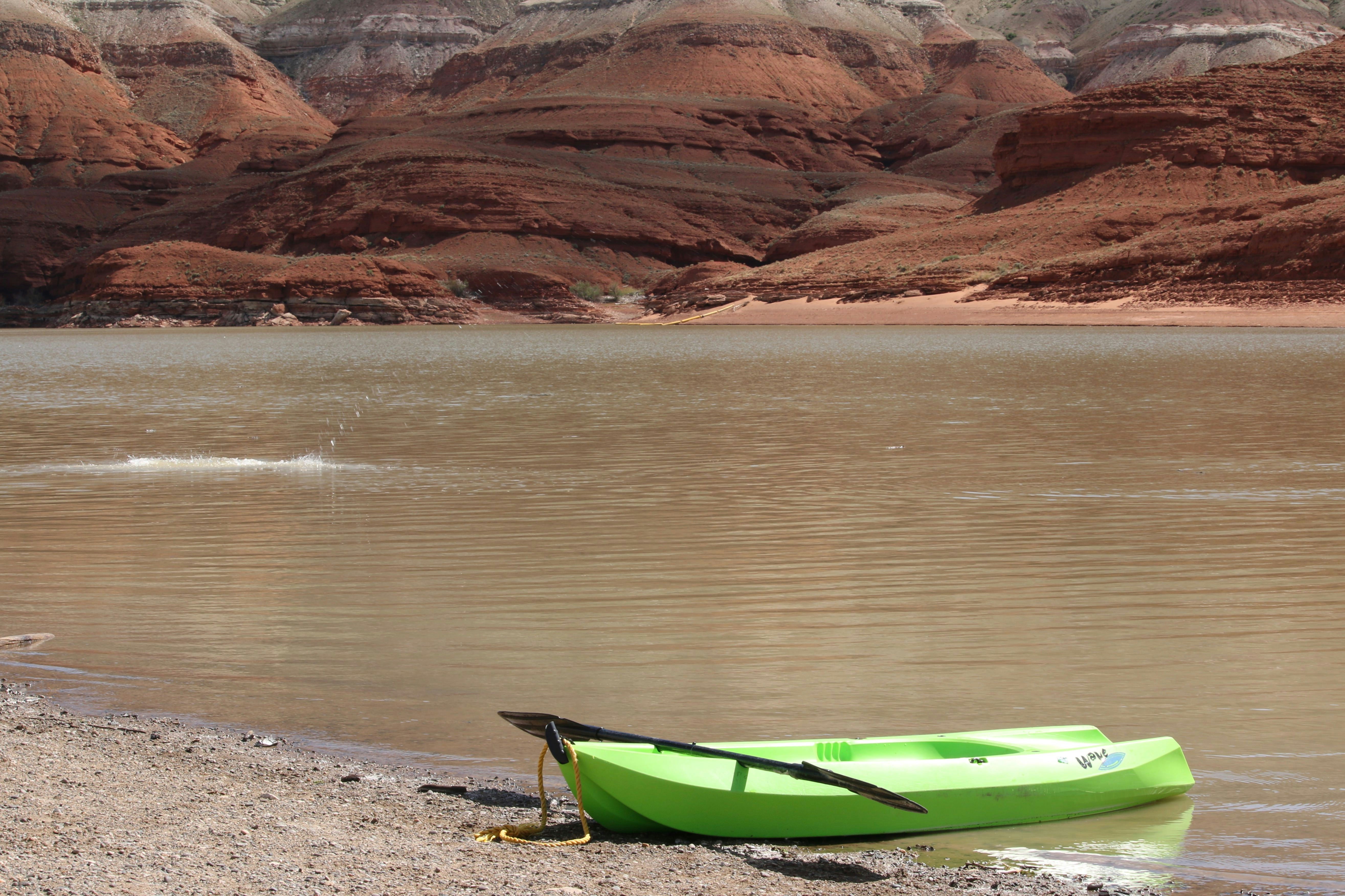 A green kayak contrasts with the red surroundings of the Horseshoe Bend Marina. | green kayak on brown sand near body of water during daytime