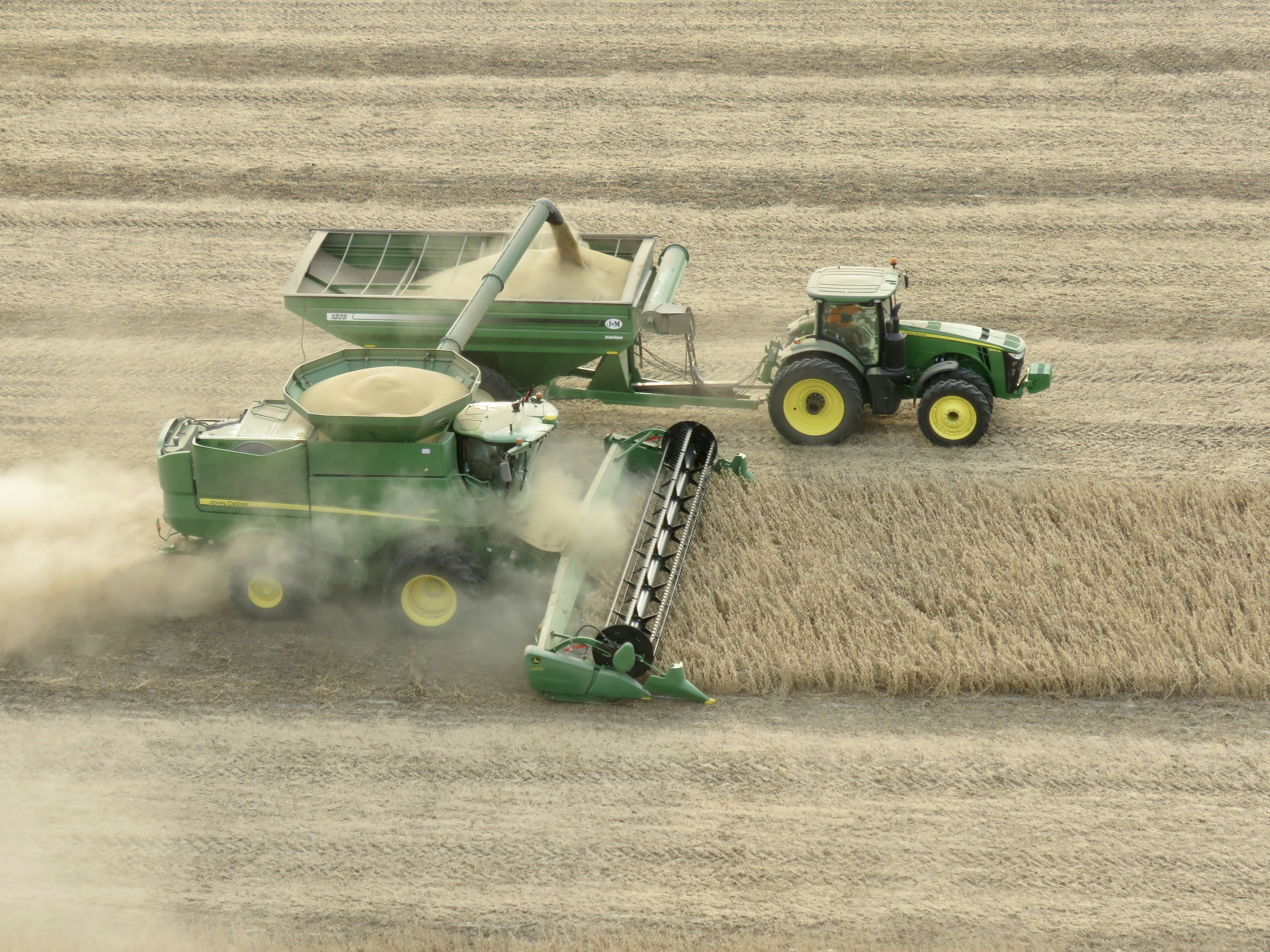 Aerial view of a combine harvester and tractor working together in a golden field, showcasing the efficiency of modern agriculture.