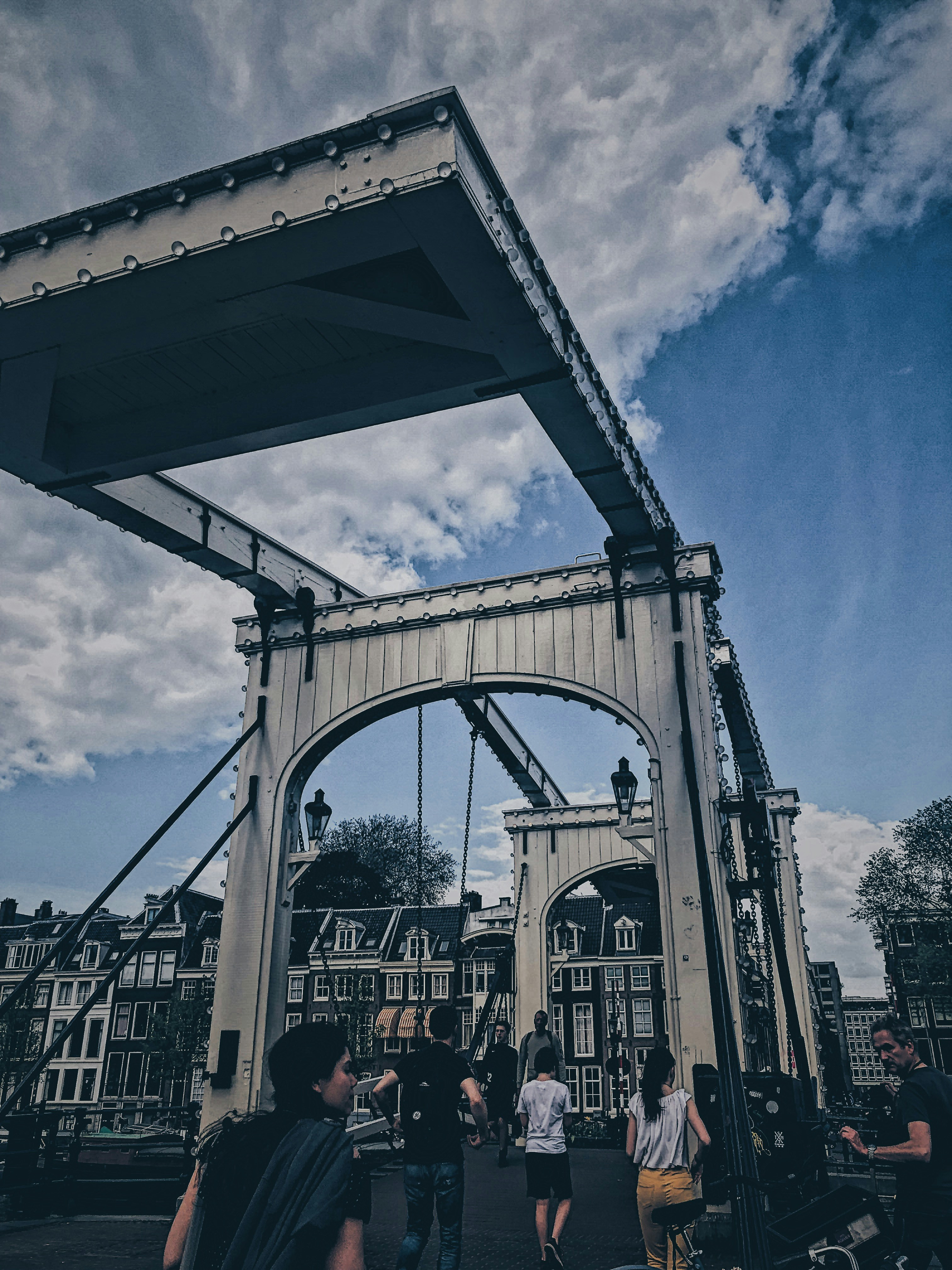 Historic drawbridge framed by a vibrant sky, with pedestrians crossing beneath its arches. The scene captures a lively urban atmosphere.