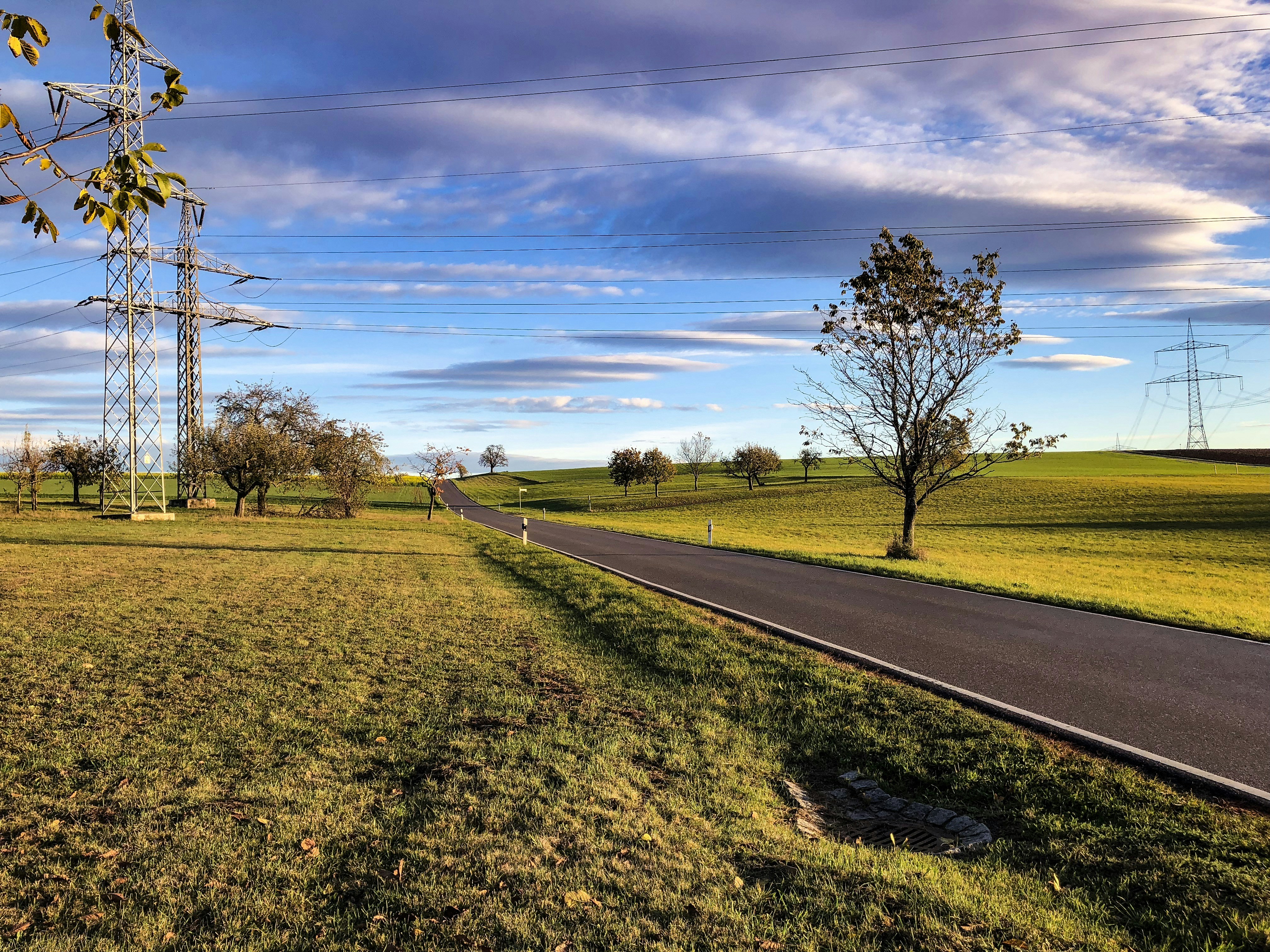 Paved road cutting through lush green fields under a vibrant blue sky with scattered clouds.