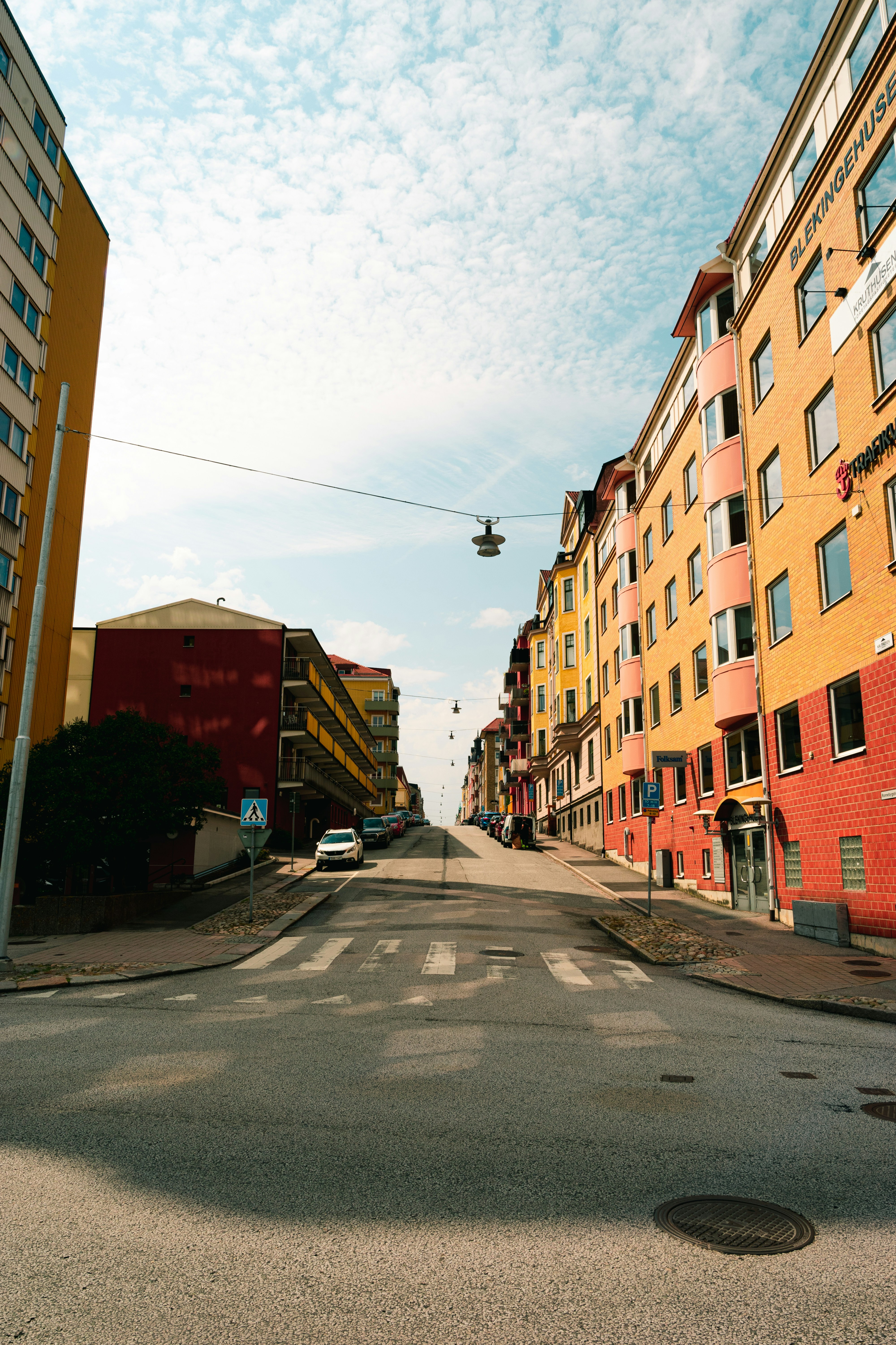 Vibrant city street lined with colorful buildings under a partly cloudy sky, showcasing urban life and architecture.