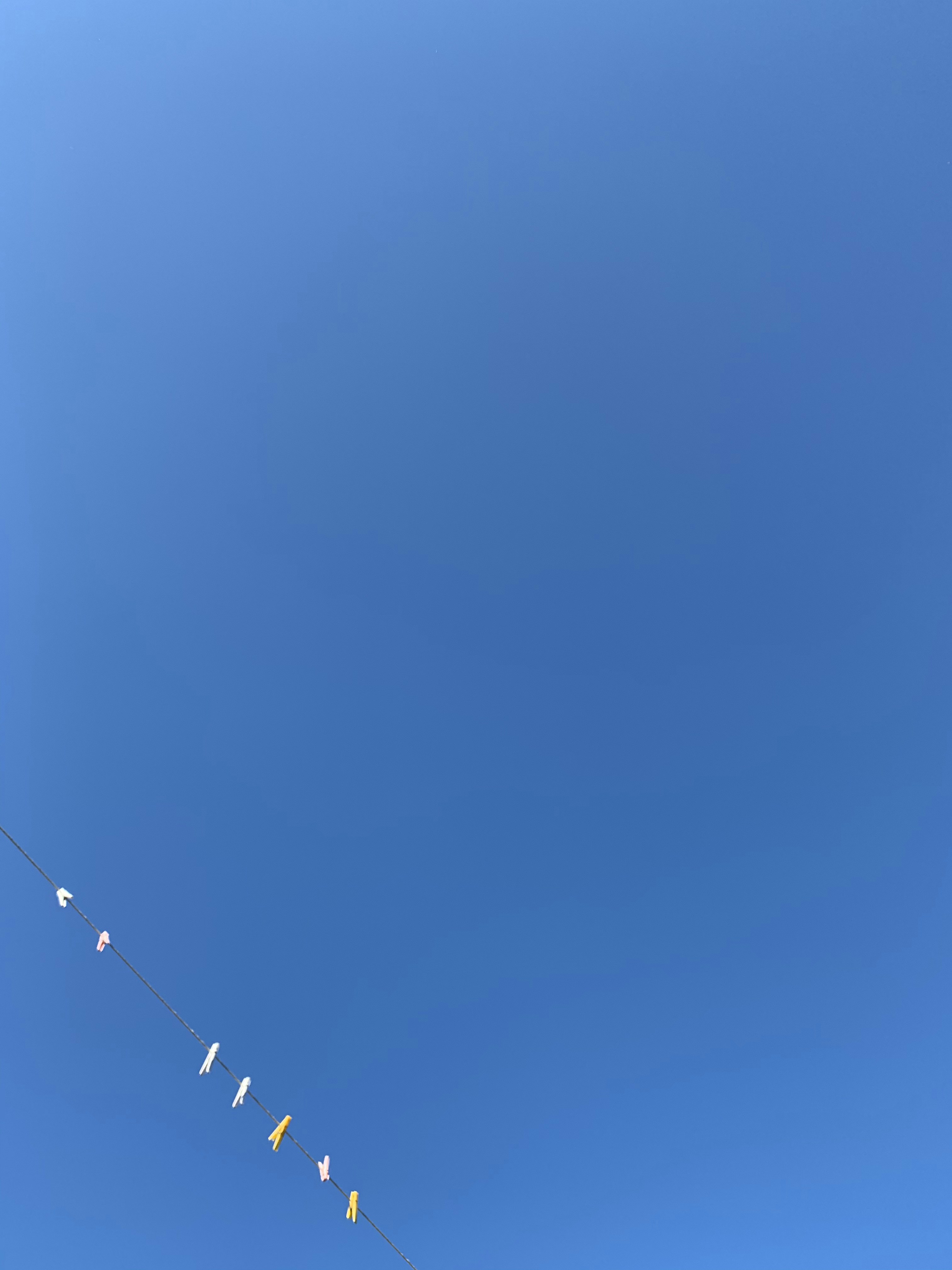Colorful clothespins hanging on a line against a clear blue sky.