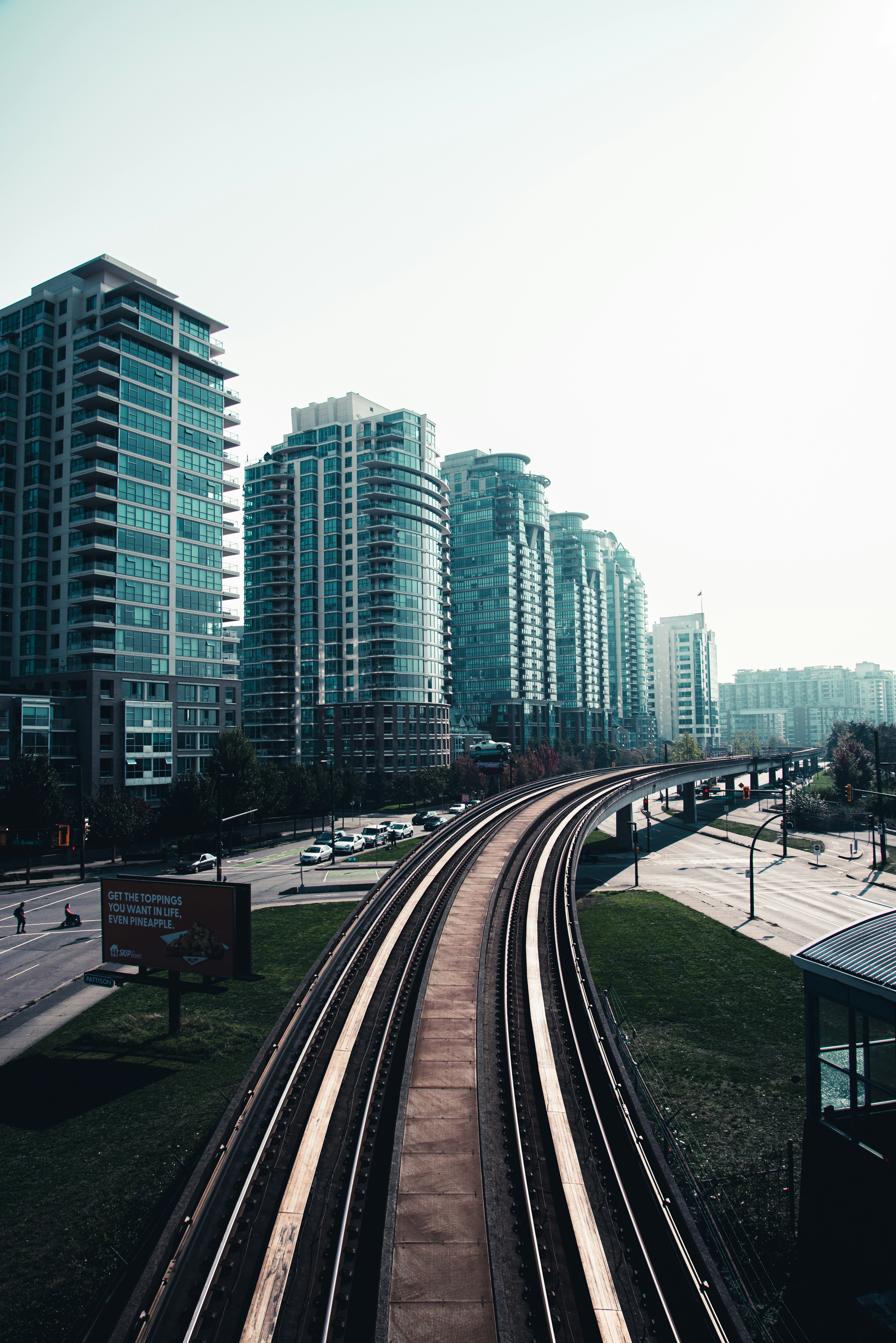Curved railway tracks weave through a modern cityscape, flanked by sleek high-rise buildings under a pale sky.