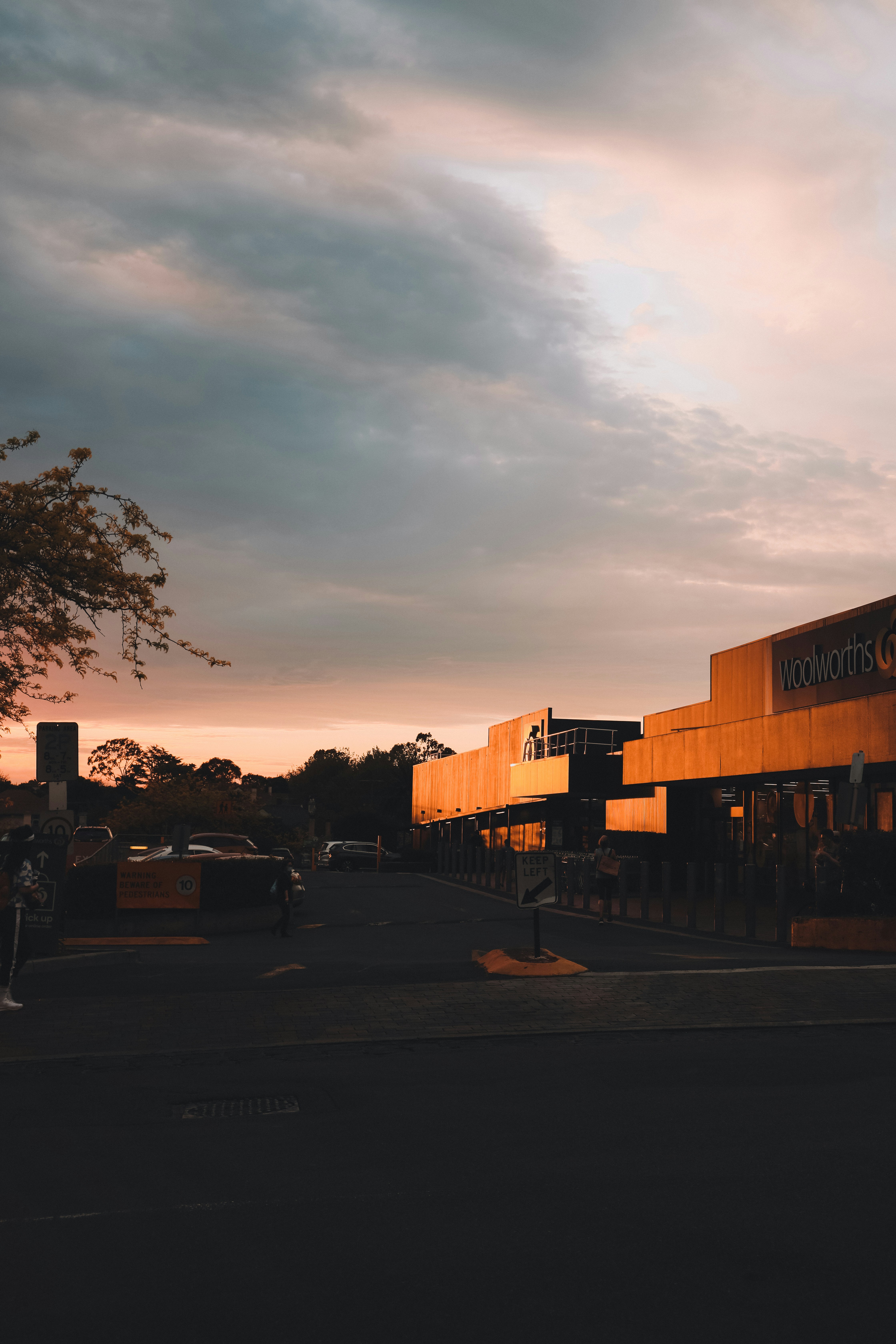Woolworths store illuminated by soft twilight, surrounded by a quiet parking lot under a dramatic sky. 