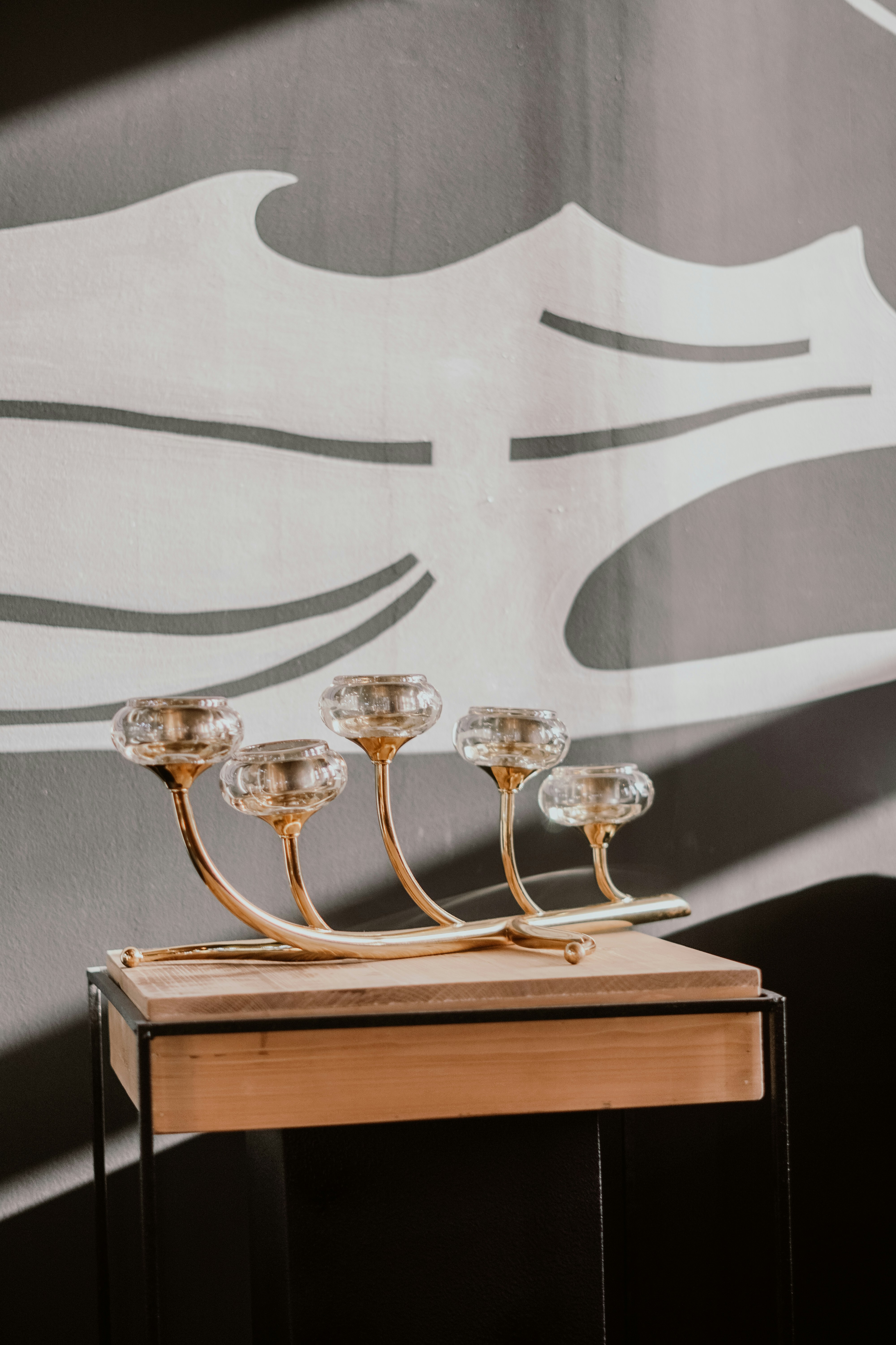 Curved Glass-Bloom Candelabrum on a Wooden Pedestal Beneath an Abstract Wall