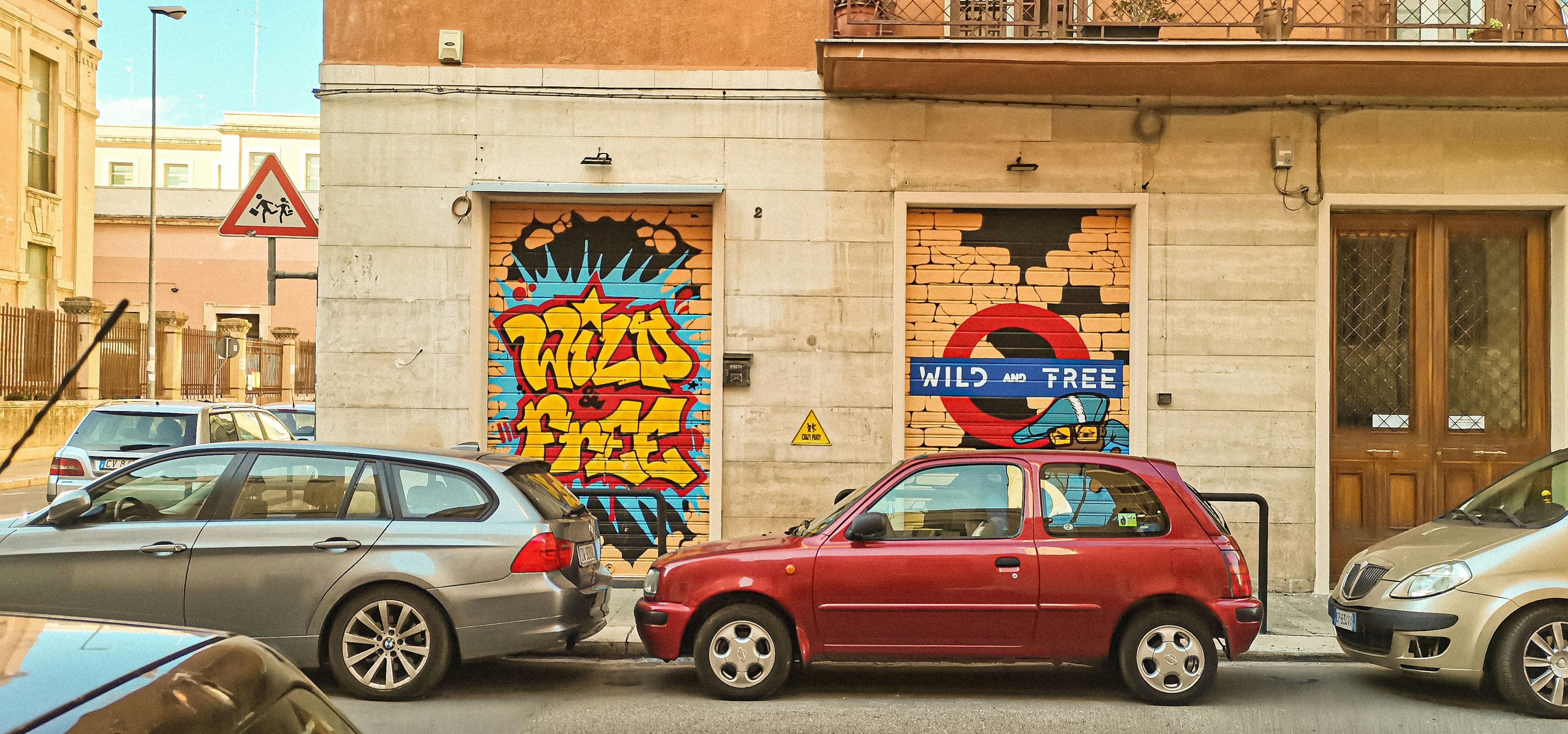 Cars parked in front of a building adorned with colorful graffiti and street art.