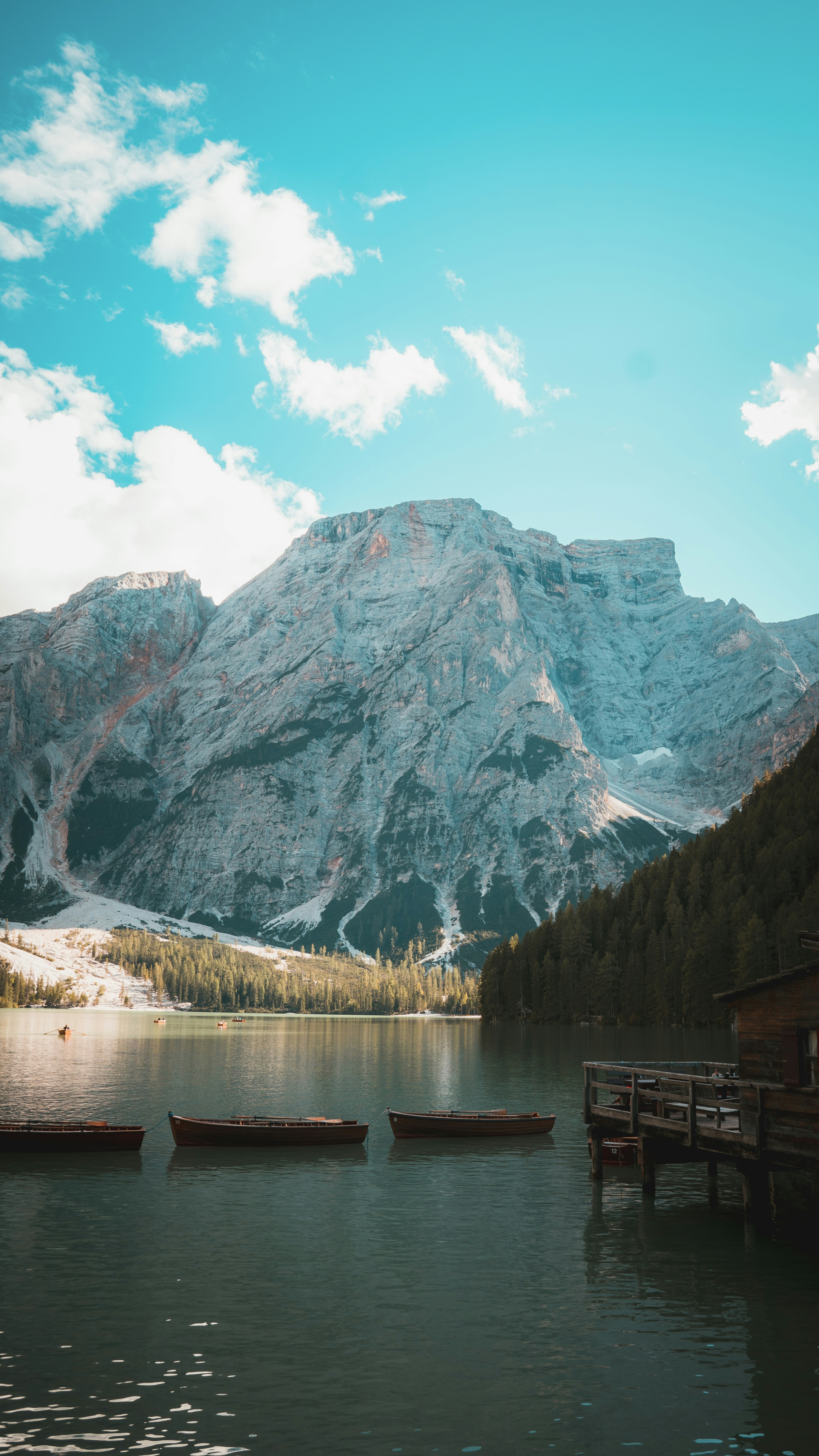 Rowboats lined along a tranquil lake with towering mountains in the background under a clear blue sky.