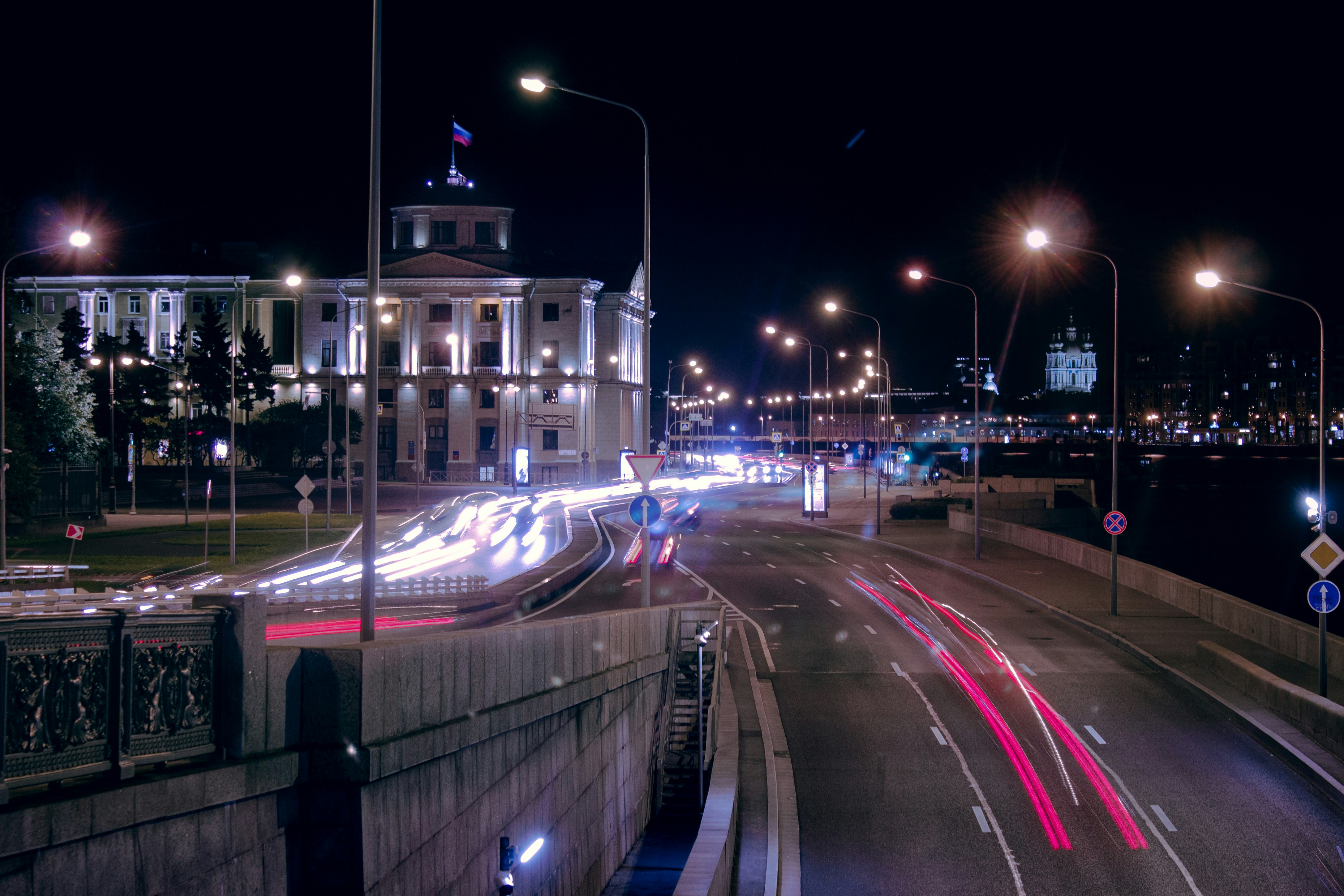 Traffic trails illuminate a cityscape at night, showcasing a blend of architecture and urban movement. The scene captures the vibrancy of nighttime city life.