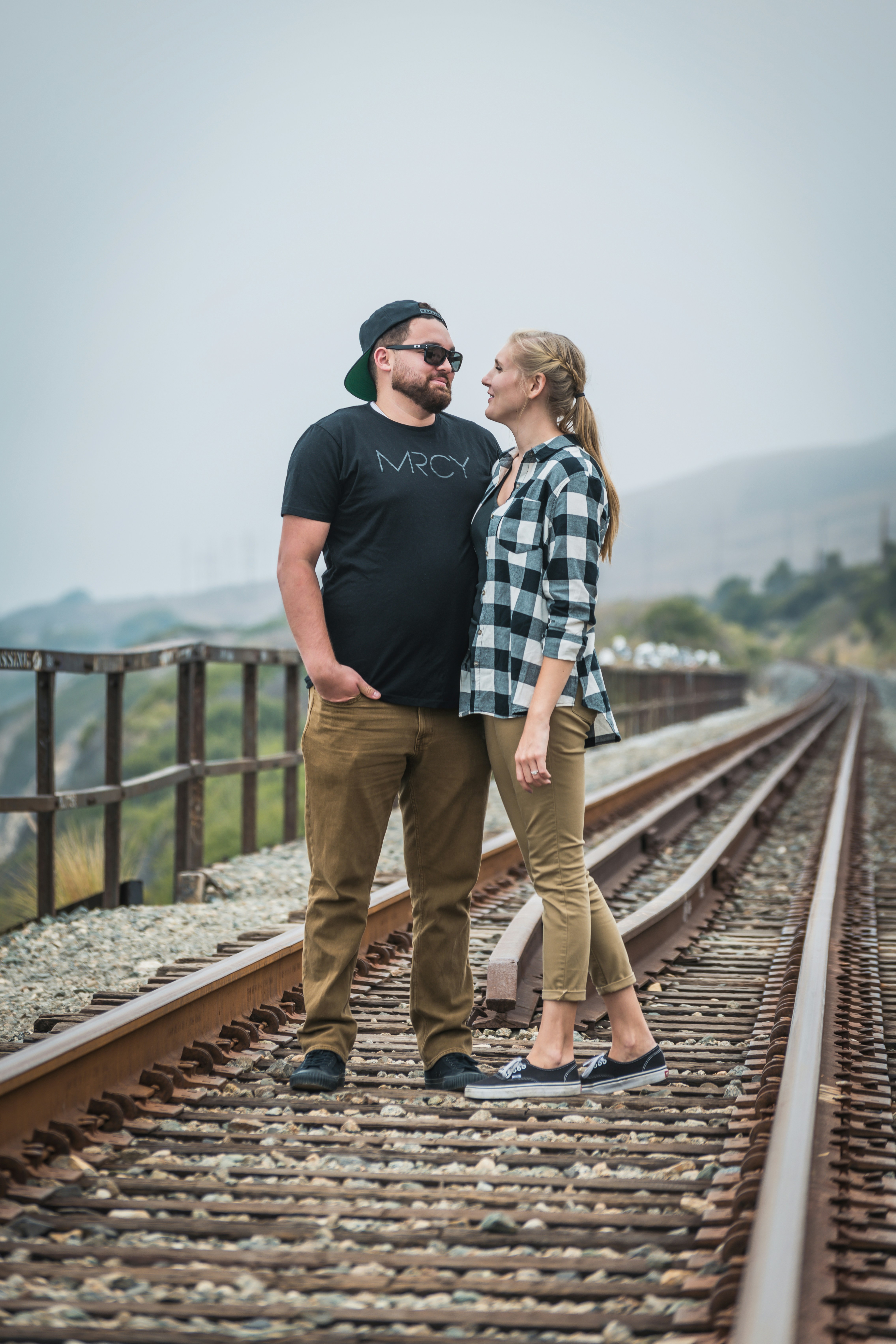 Couple standing closely on a railway track, exuding warmth and connection amidst a serene backdrop.