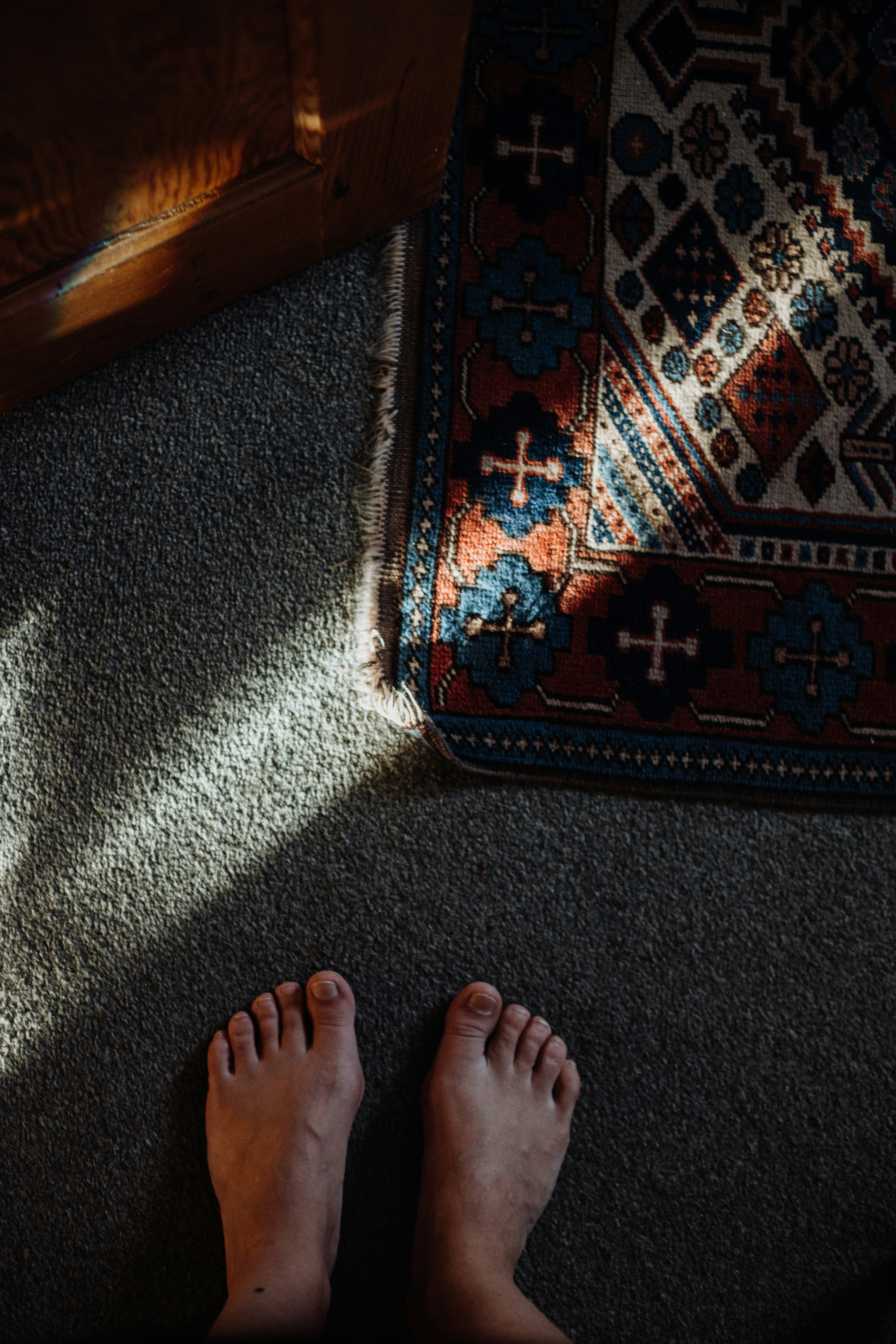 Bare feet resting on a textured carpet, with a colorful rug casting soft shadows in warm light.