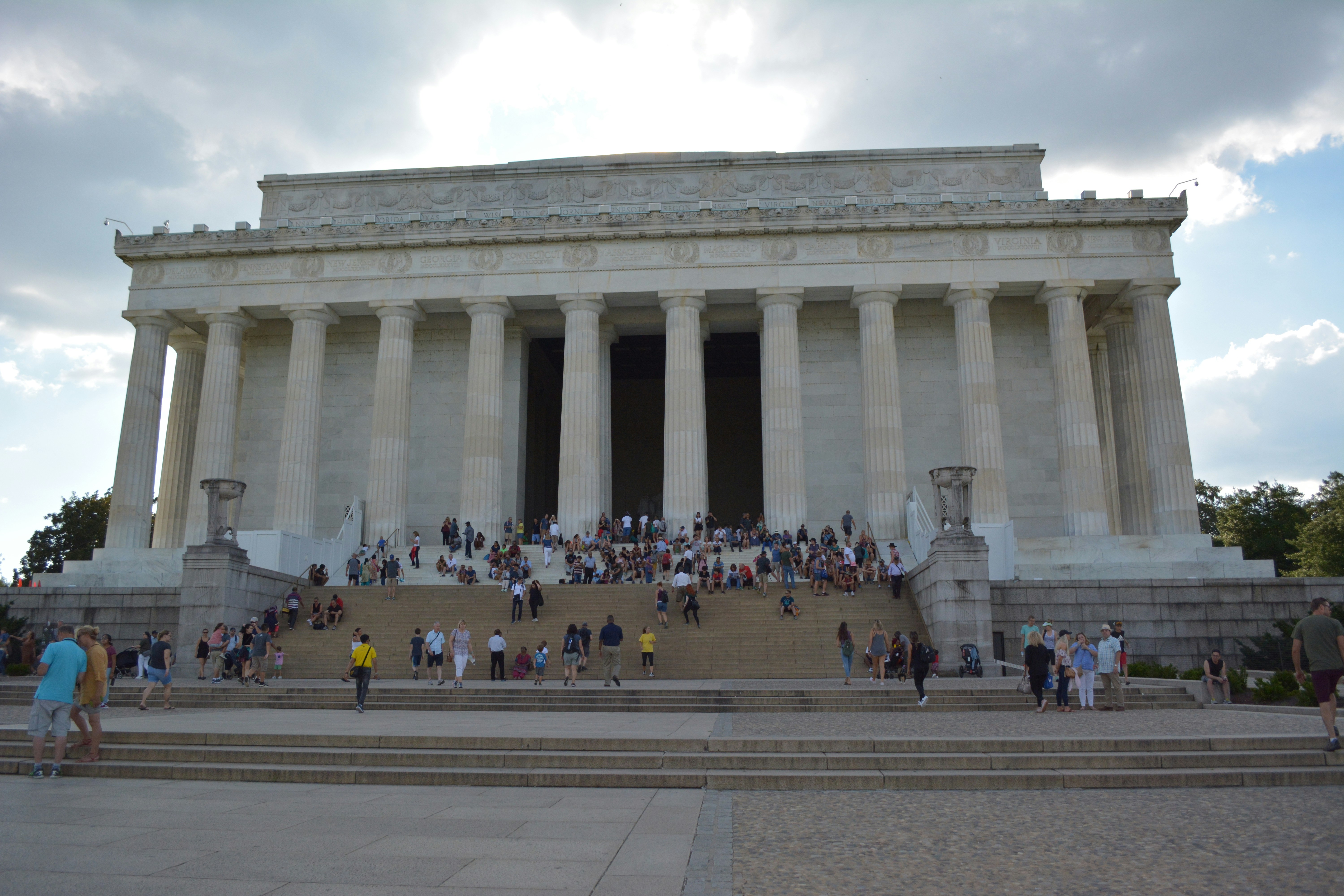 Lincoln Memorial with visitors on its grand steps, under a partly cloudy sky.
