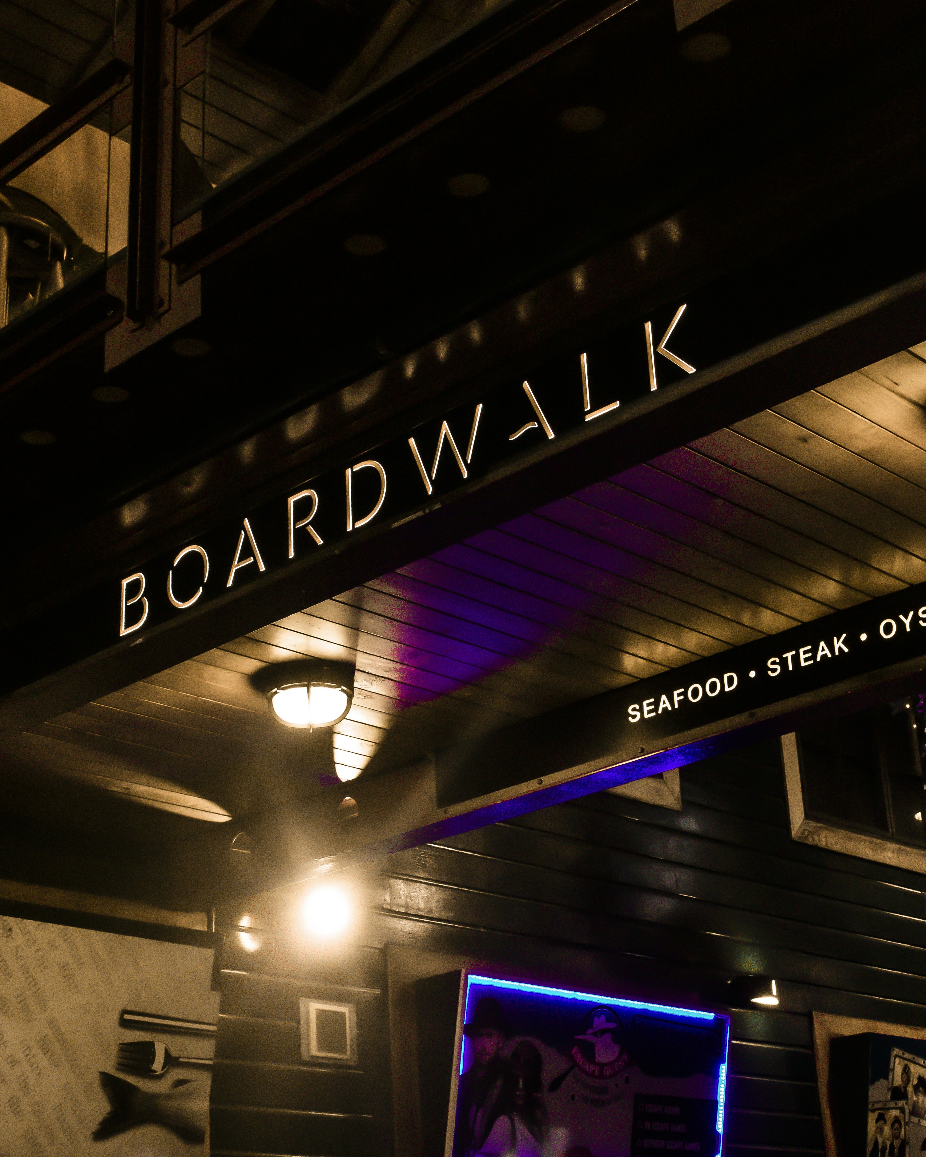 Illuminated sign for 'BOARDWALK' with a cozy ambiance, featuring a seafood and steak menu. Soft lighting enhances the inviting atmosphere.