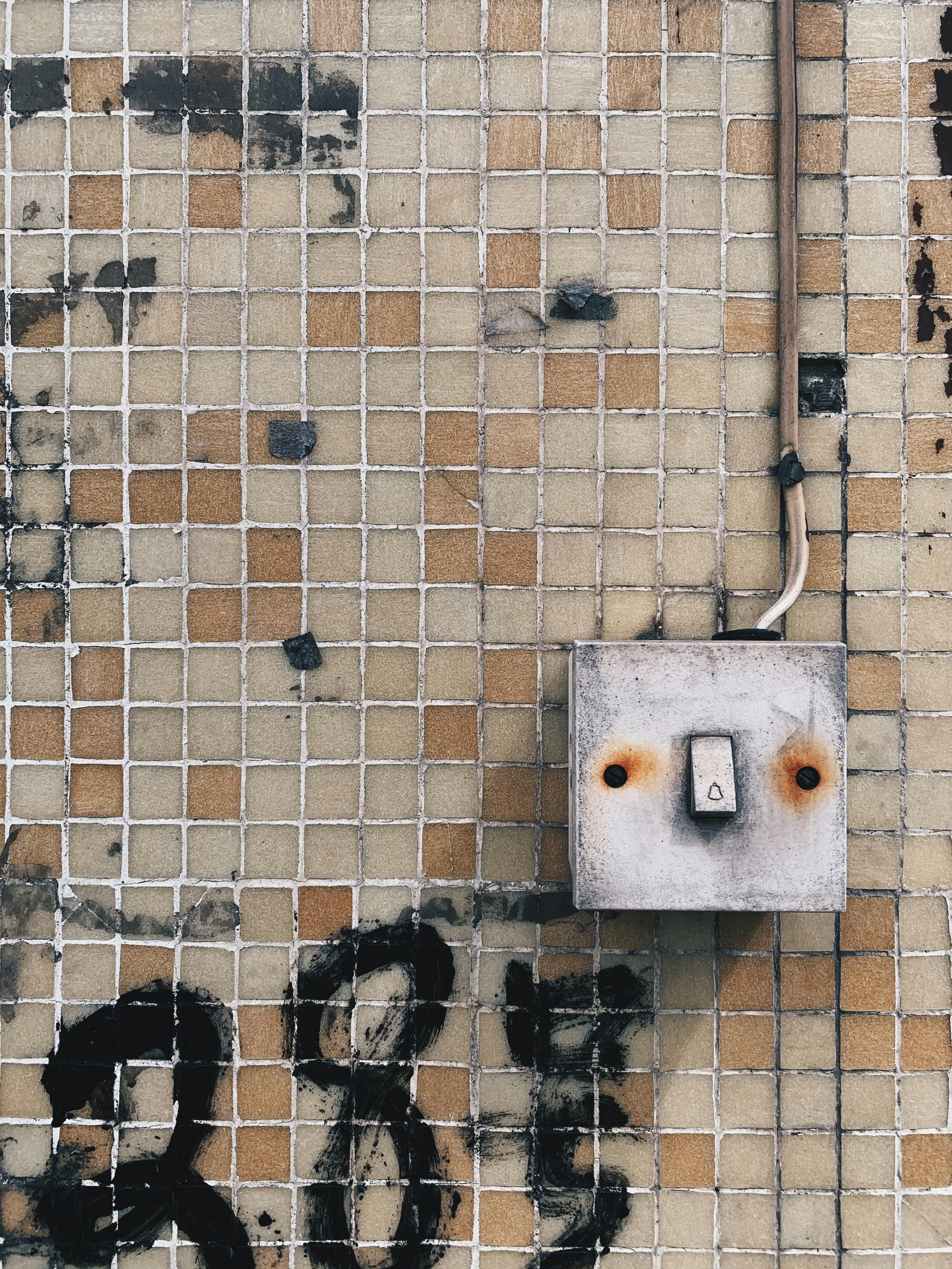 Aged Gridwork: The solitary switch on a weathered tiled facade