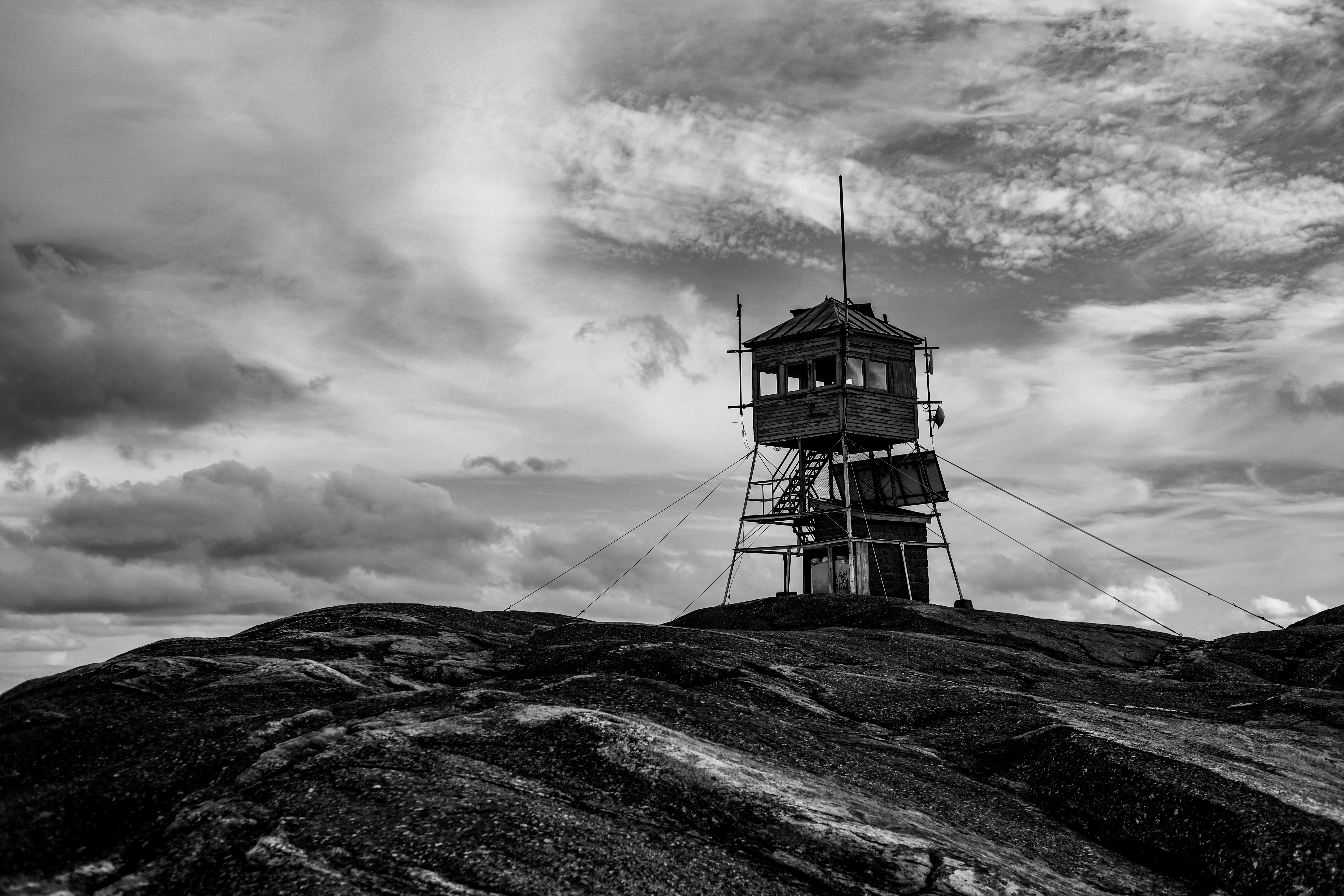 A solitary watchtower stands atop rugged terrain, framed by dramatic clouds in a monochrome palette. The structure exudes a sense of isolation and resilience.