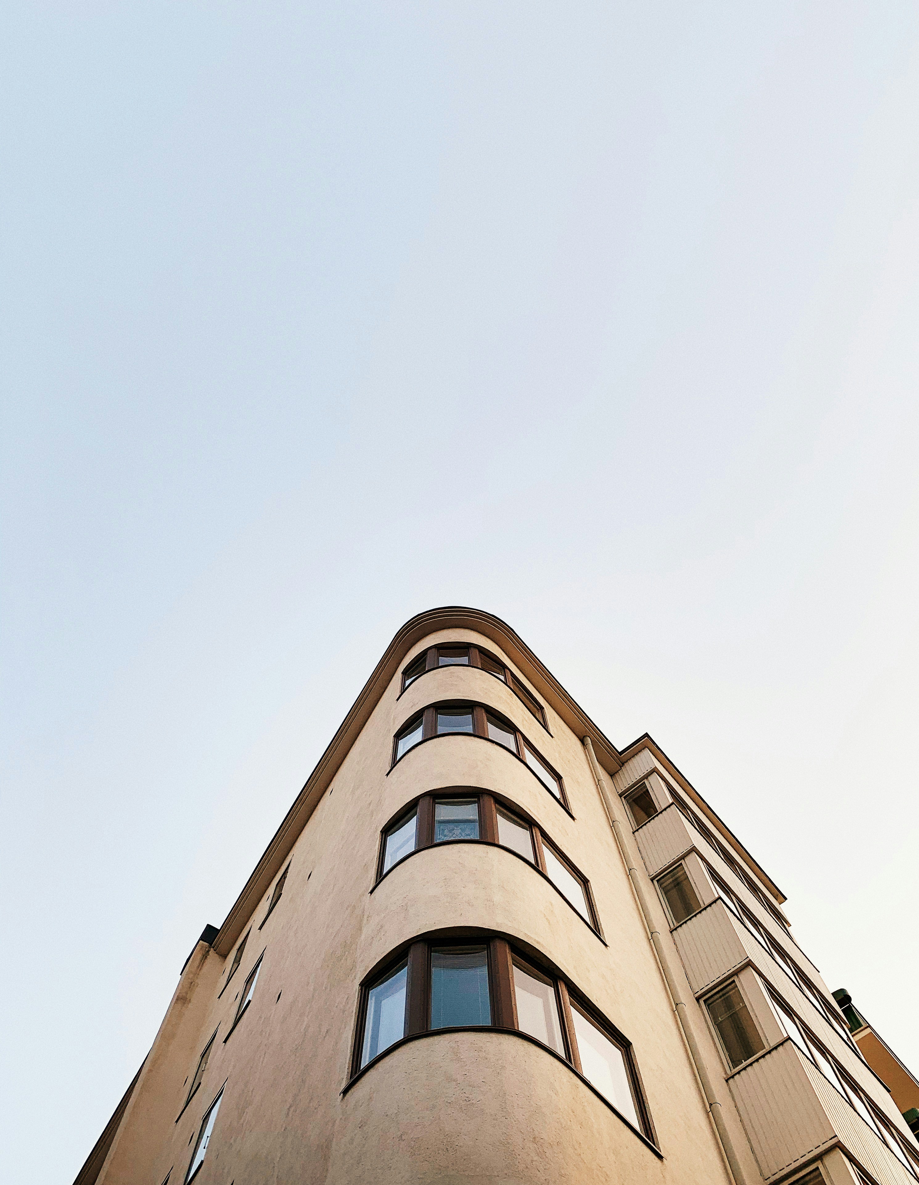 Curved corner of a brown concrete apartment building against a clear white sky.