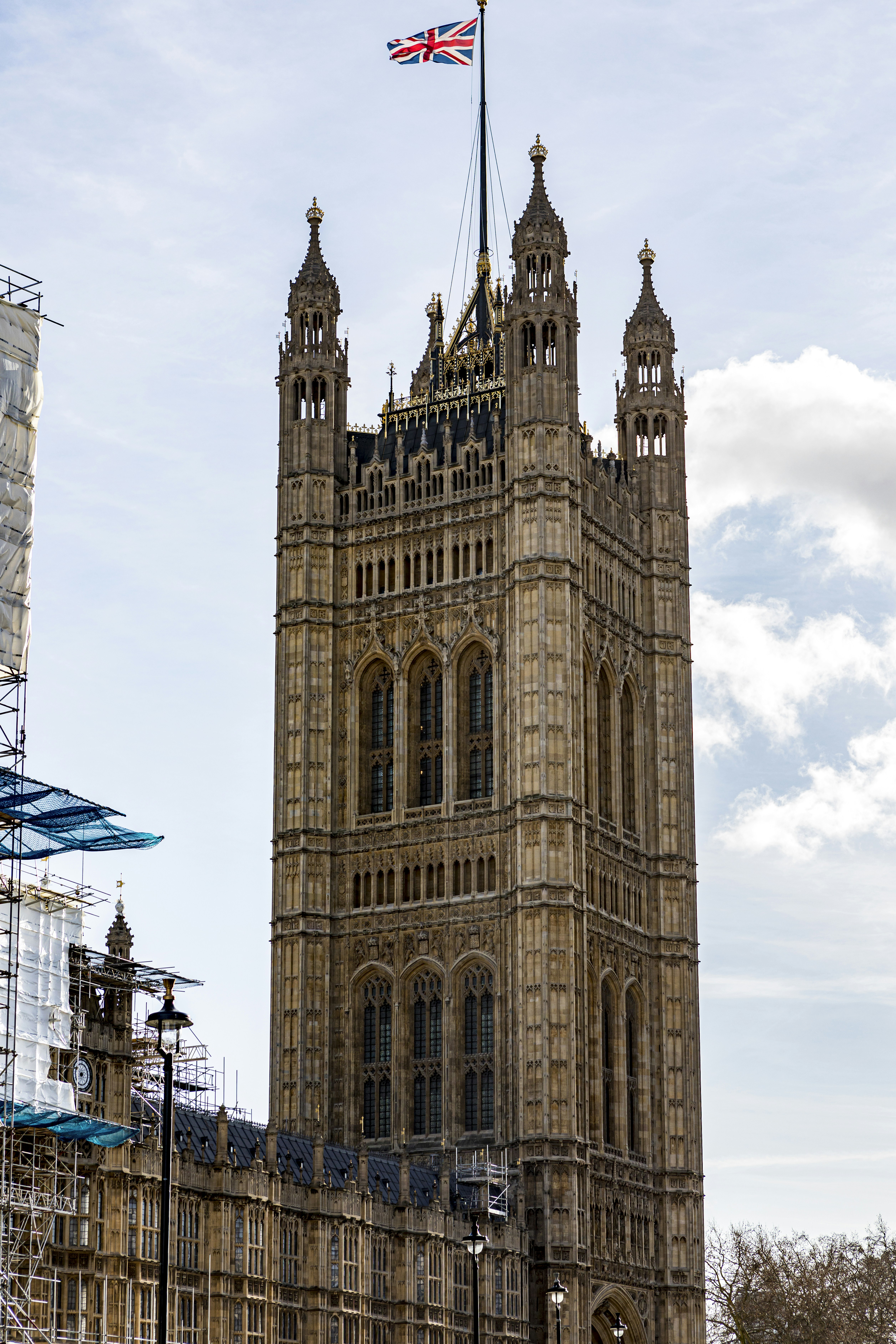 The iconic clock tower of the Palace of Westminster, adorned with the Union Jack, stands proudly amidst renovation scaffolding. A blend of historical architecture and modern preservation efforts.