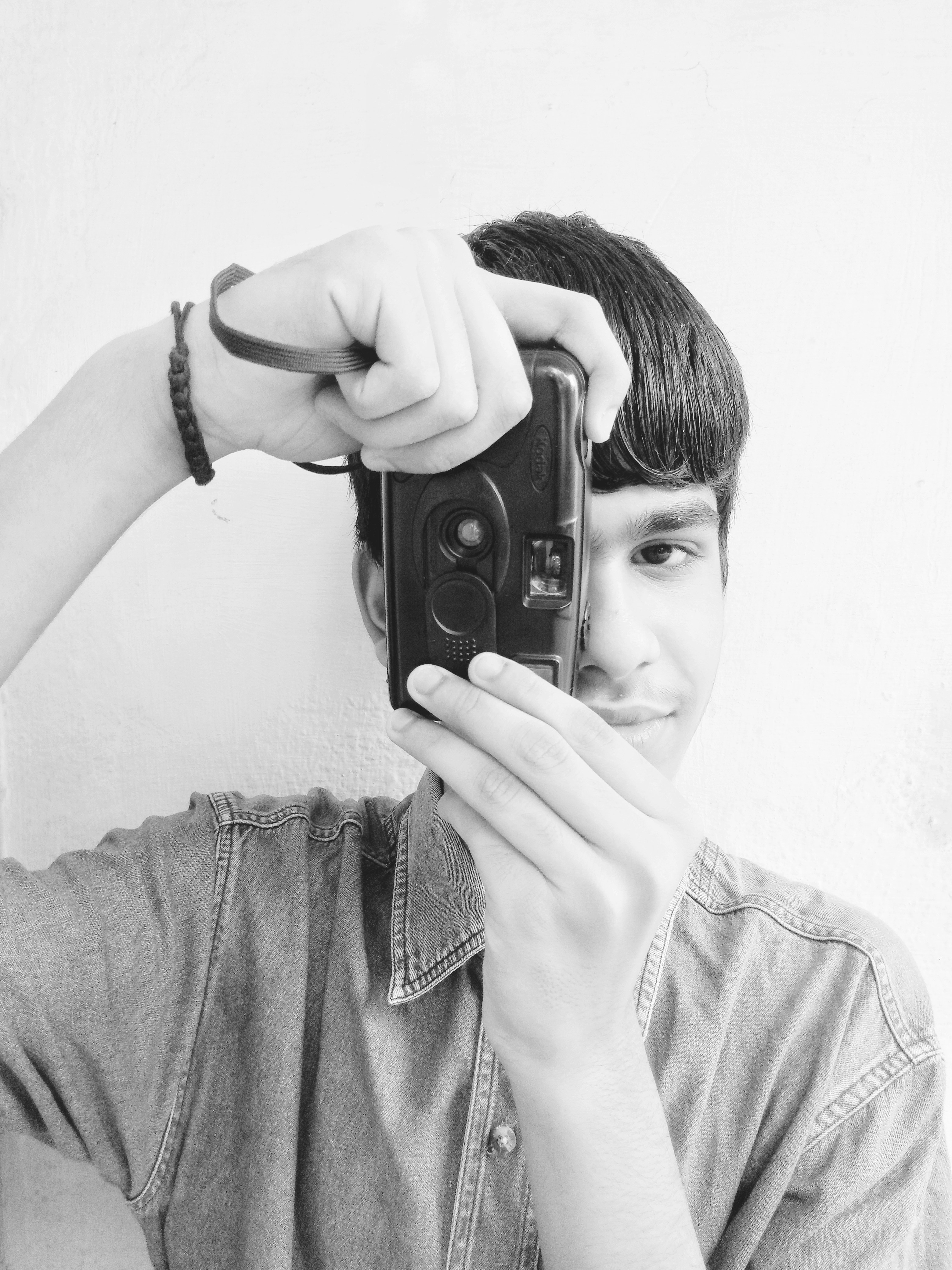 A young person holds a vintage camera up to their face in a monochrome photograph.