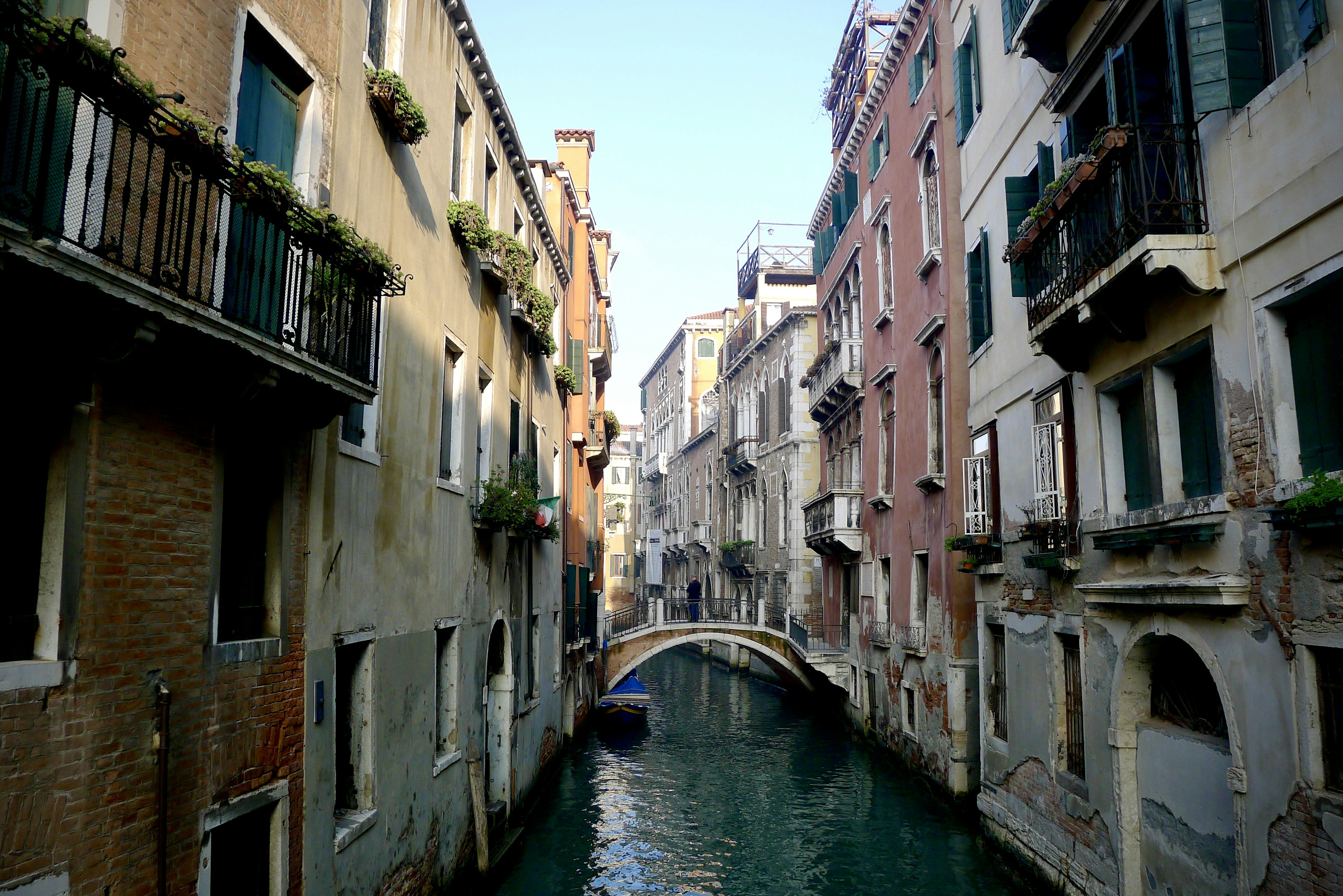 Charming canal flanked by historic buildings adorned with balconies and greenery in Venice, Italy. The gentle arch of the bridge adds to the tranquil atmosphere.