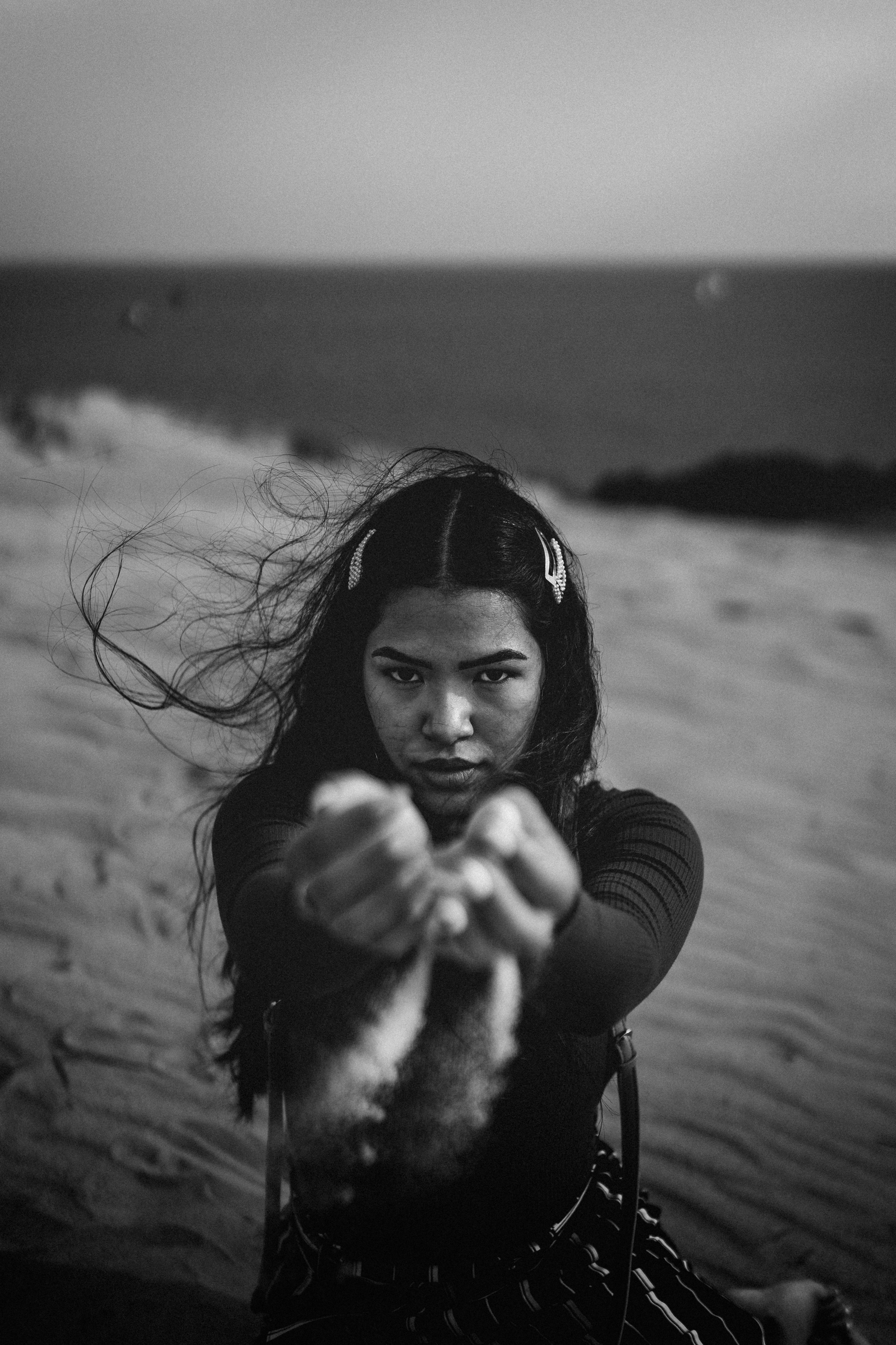 A woman extends her hands, releasing grains of sand against a backdrop of the ocean, capturing a moment of connection with nature.