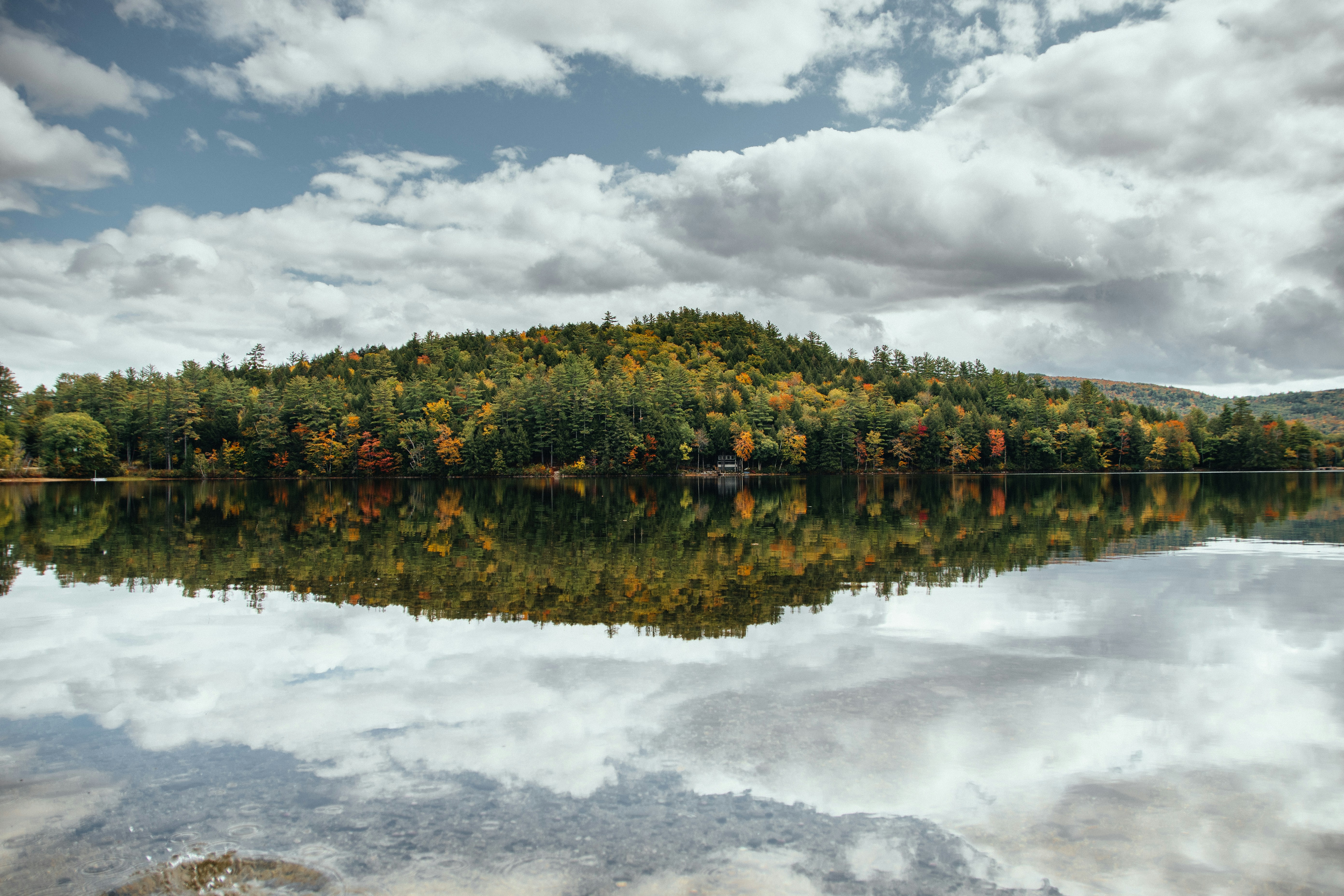 Vibrant autumn foliage mirrored perfectly in a calm lake under a cloudy sky.