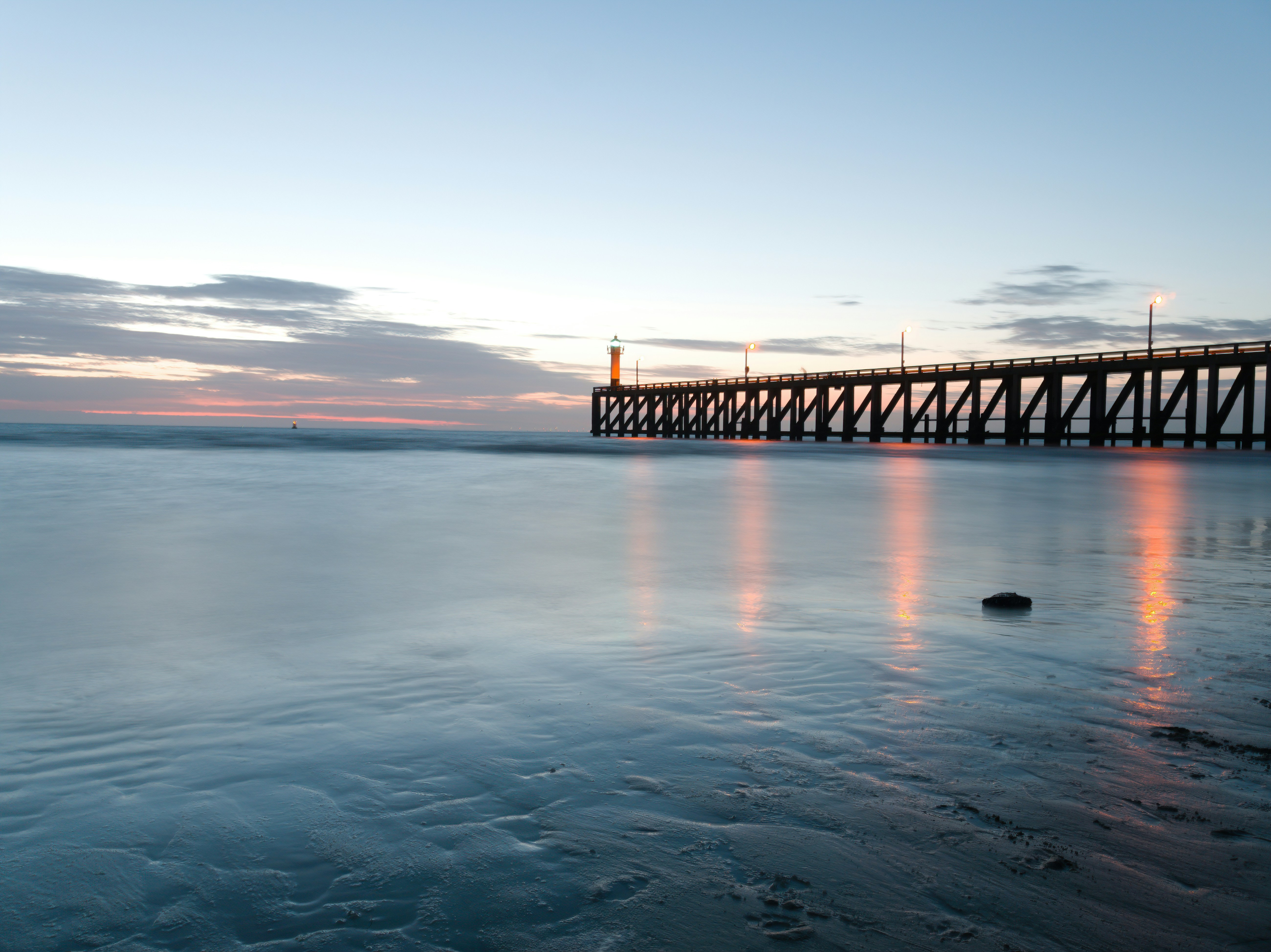 Long pier extending into calm waters under a twilight sky with soft reflections.