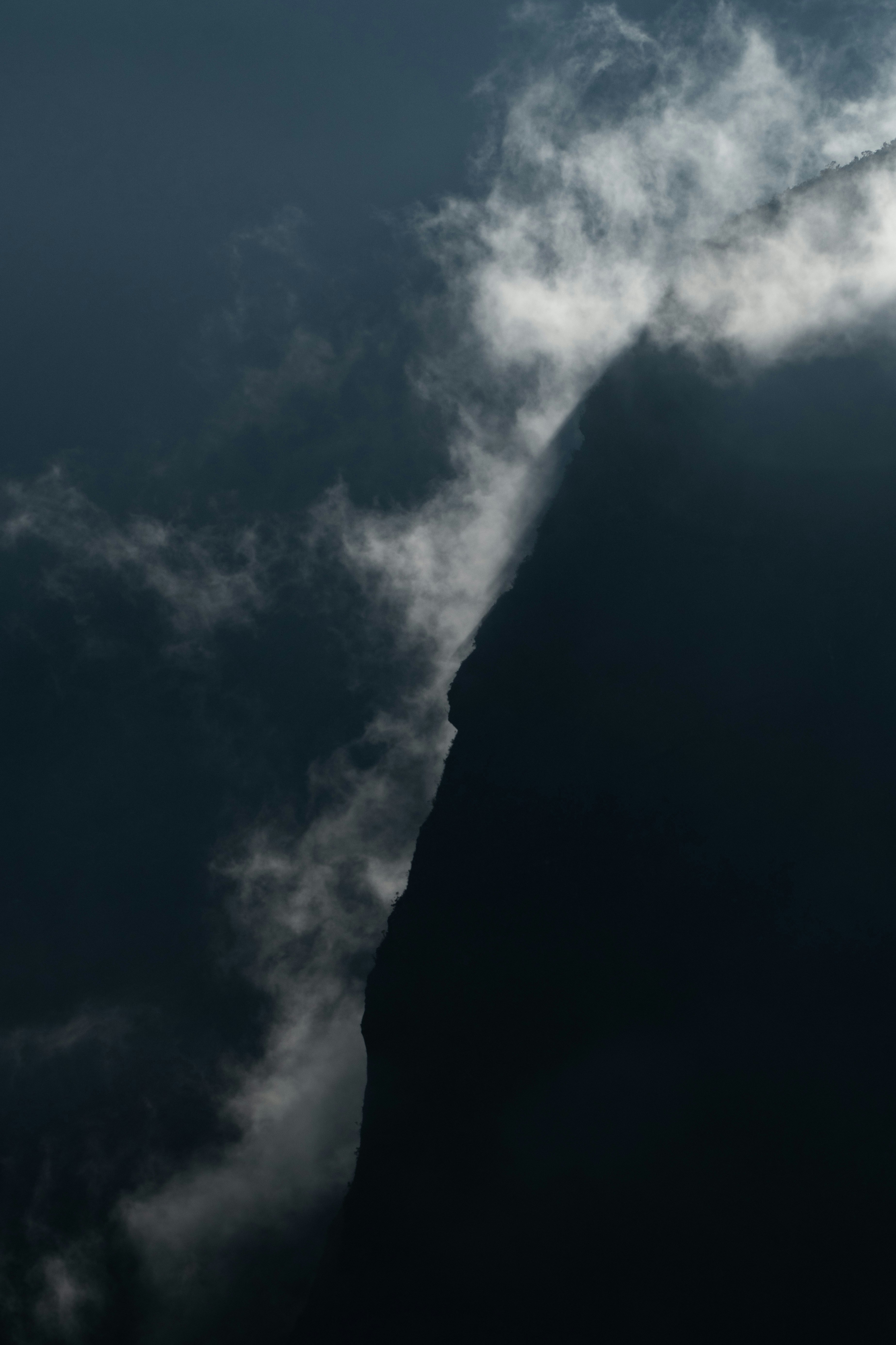 Dark mountain peak shrouded in wispy clouds under a moody sky.