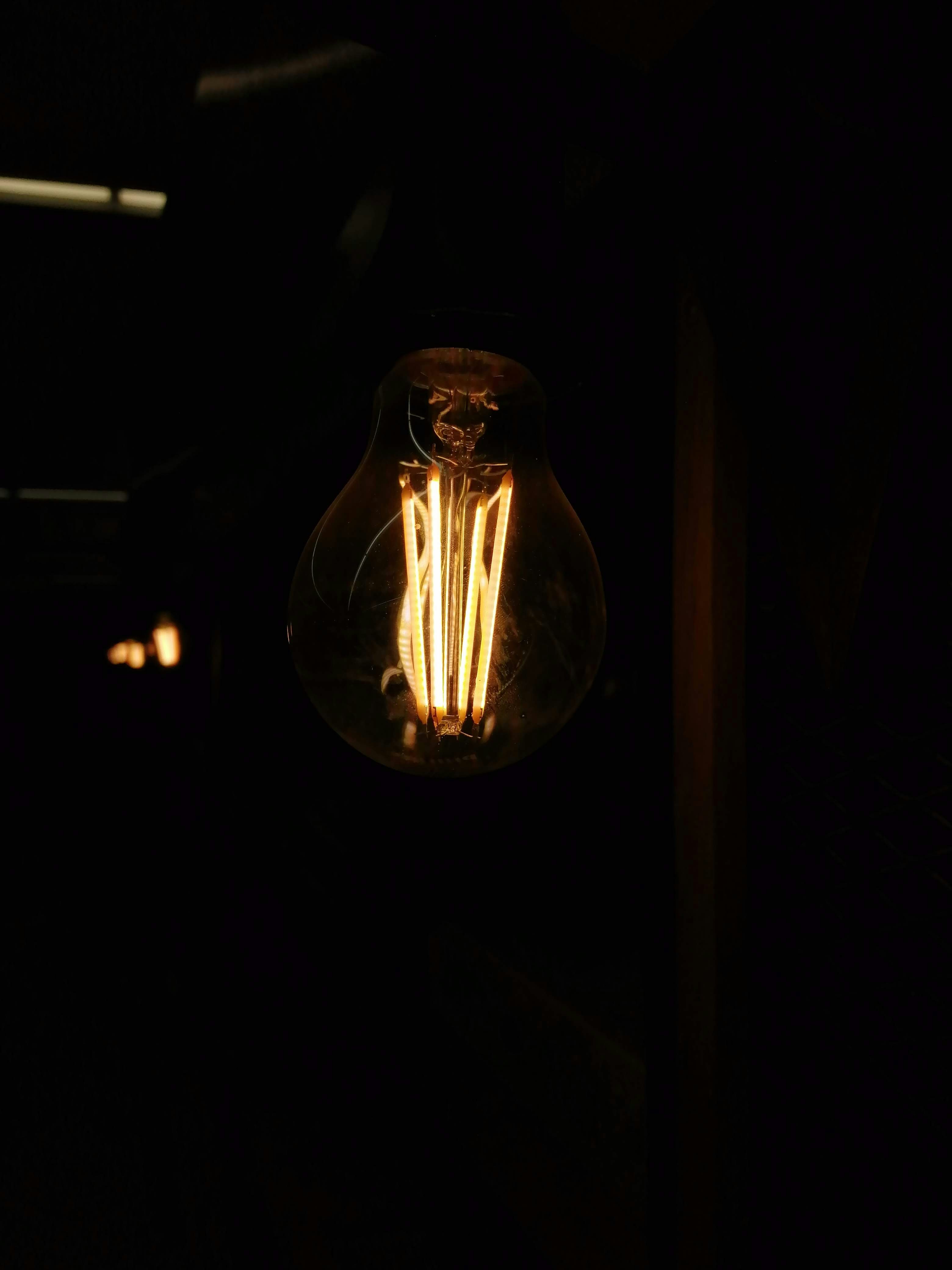 Close-up of a glowing vintage light bulb, showcasing its intricate filament design against a dark background.