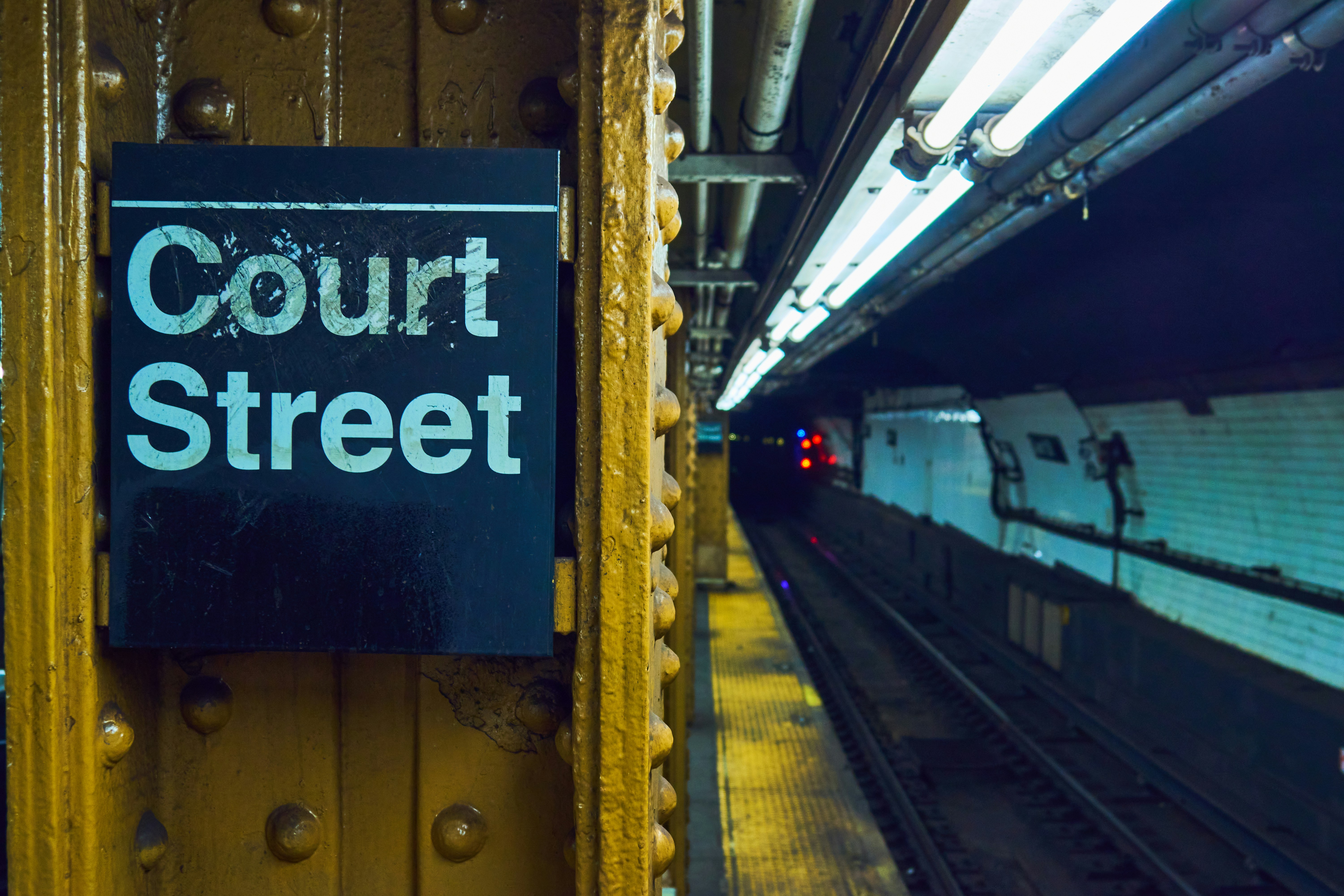 Dimly lit subway platform with a Court Street sign and a tunnel vanishing into darkness.