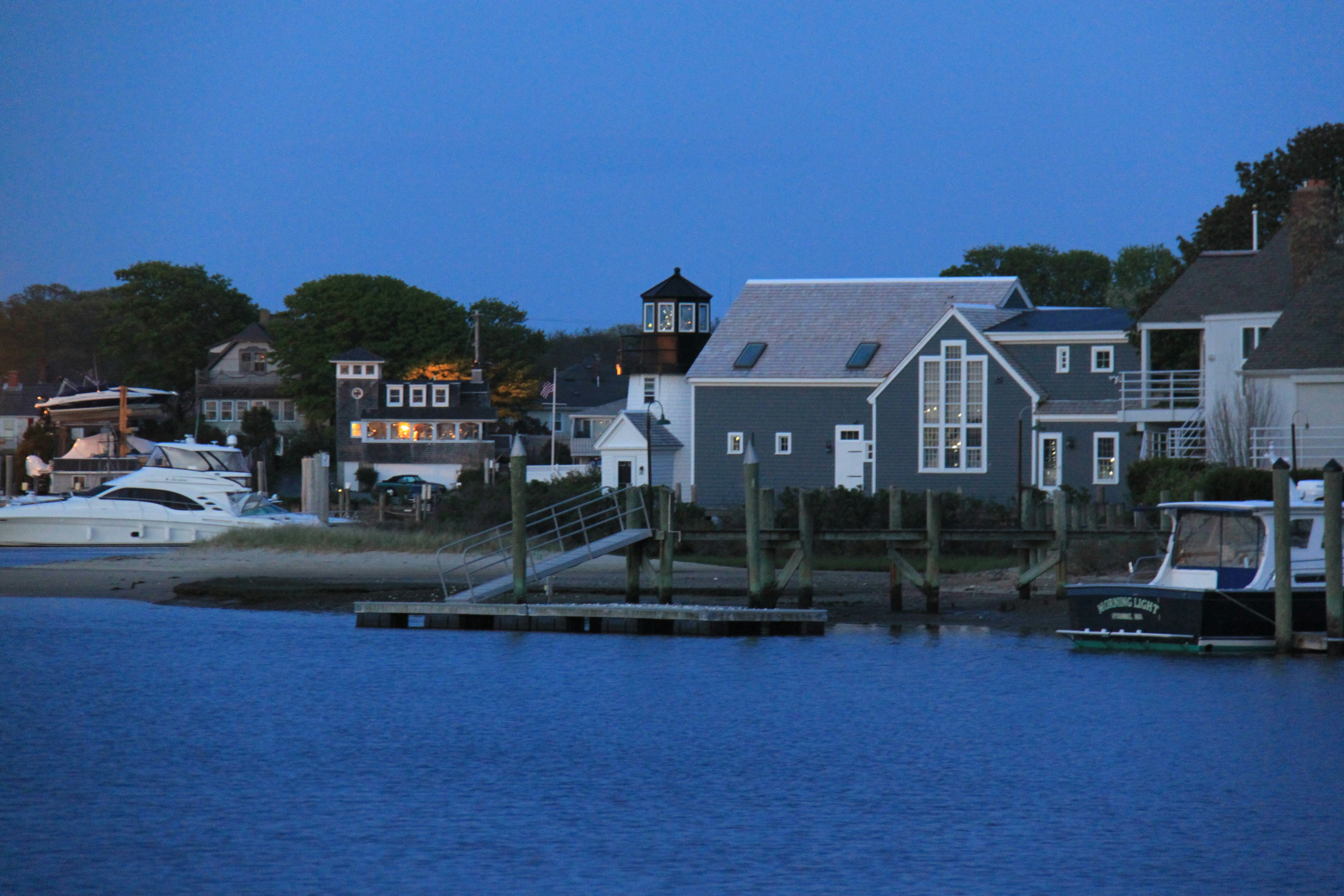 Charming coastal homes and boats reflect in the calm waters under a twilight sky.