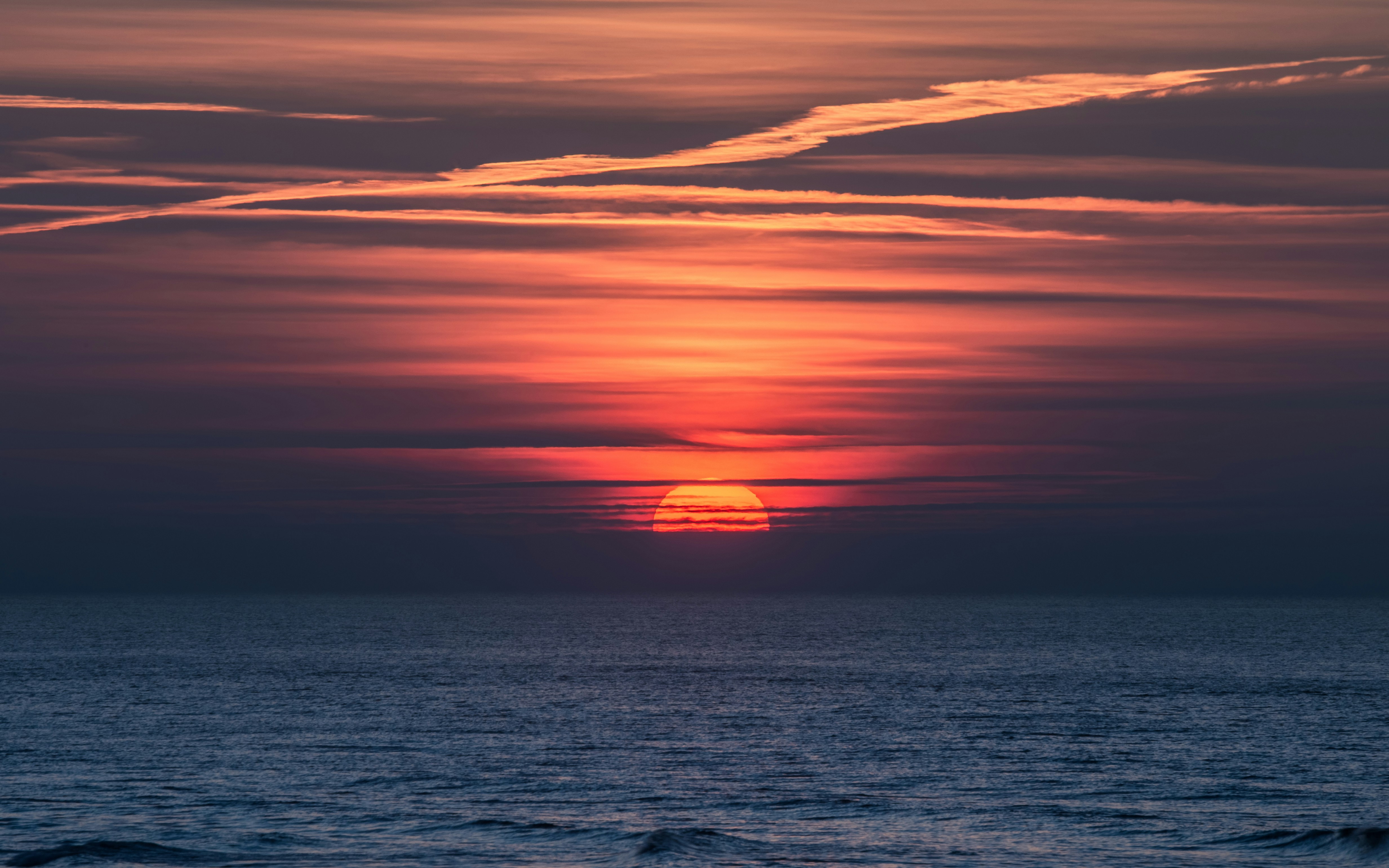 Sunset casts vibrant hues across the ocean horizon with streaked clouds in the sky.