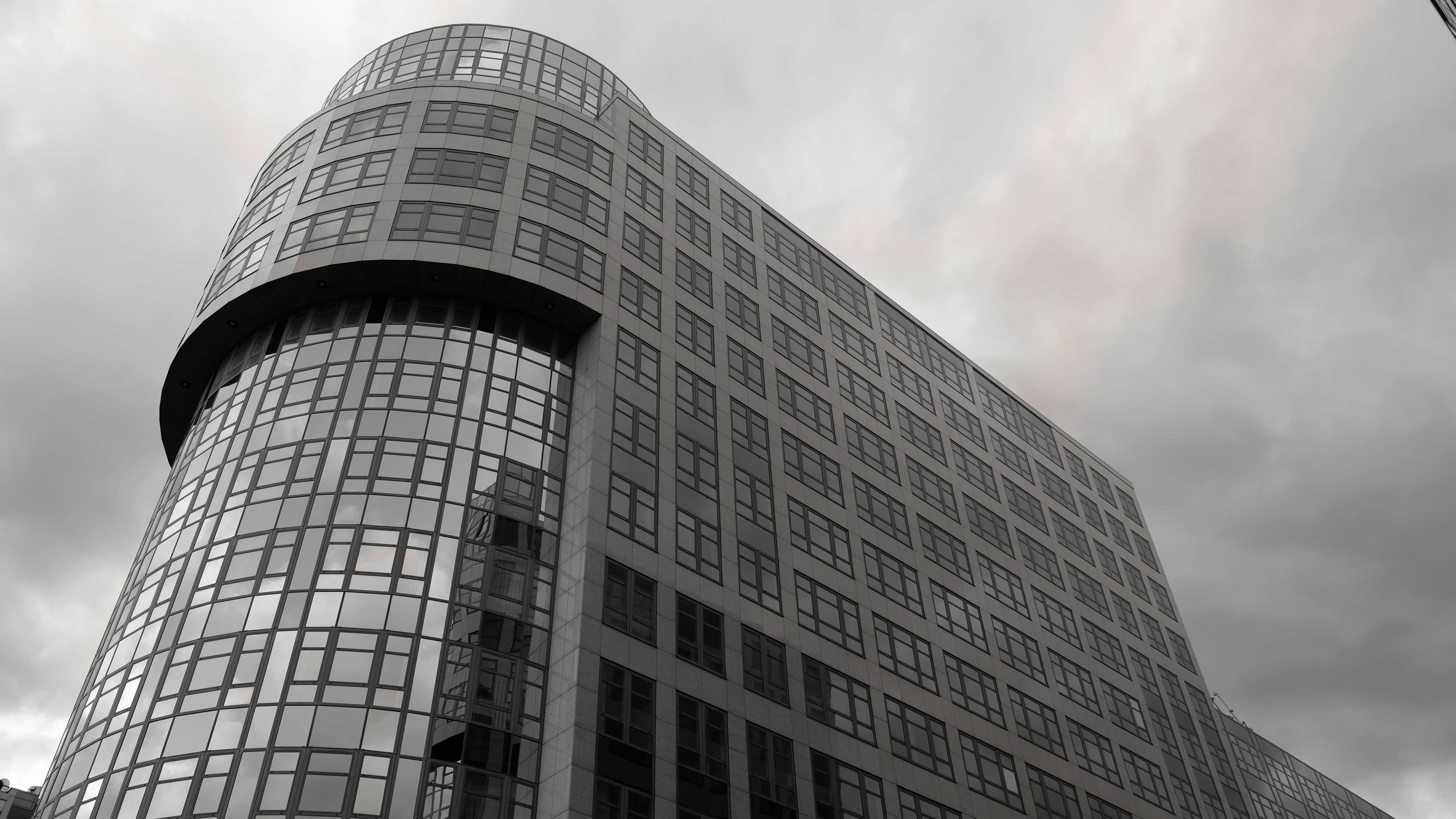 Modern glass and steel building with curved facade against a cloudy sky.
