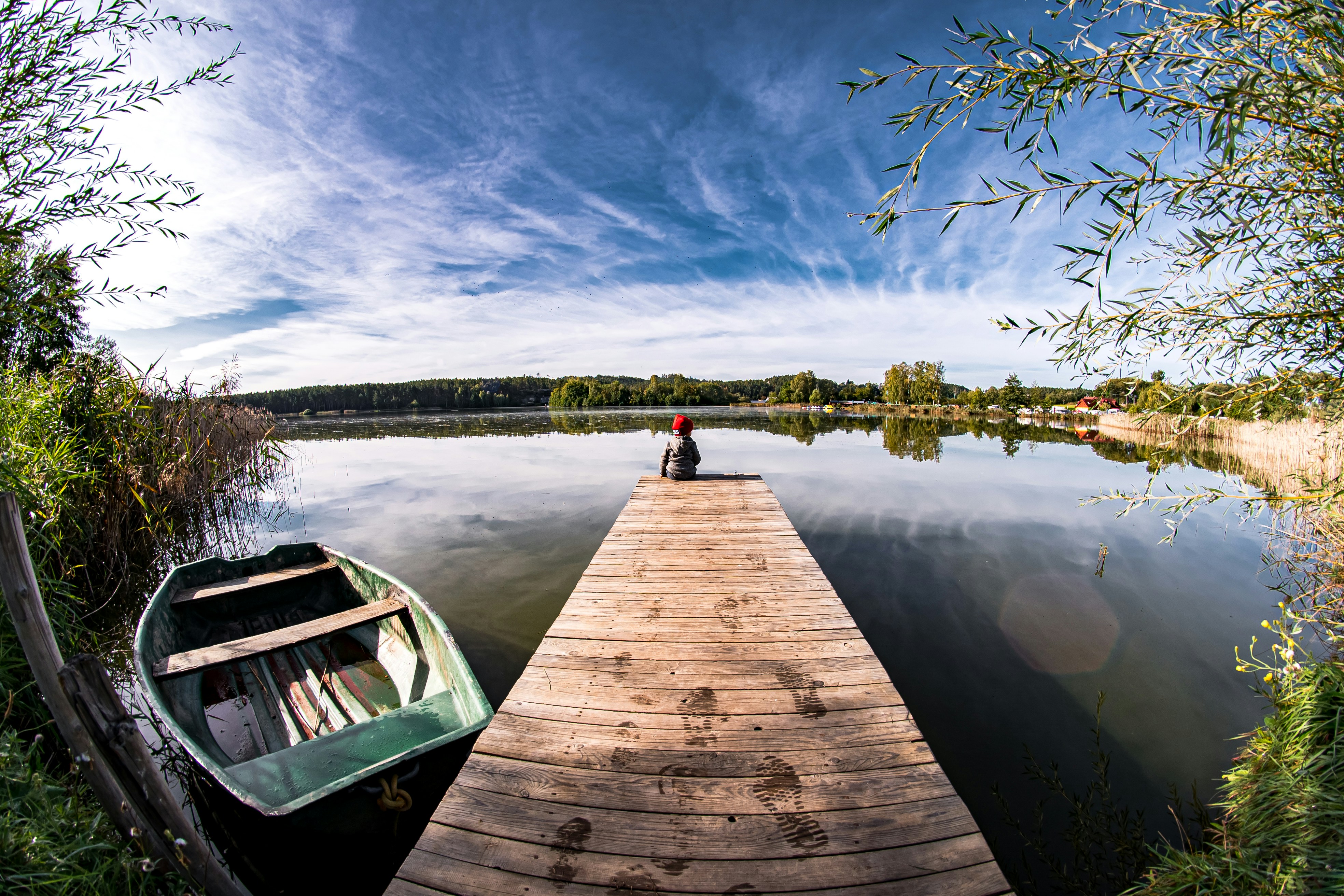 Calm Confluence: solitary figure at the end of a weathered dock over a glassy lake