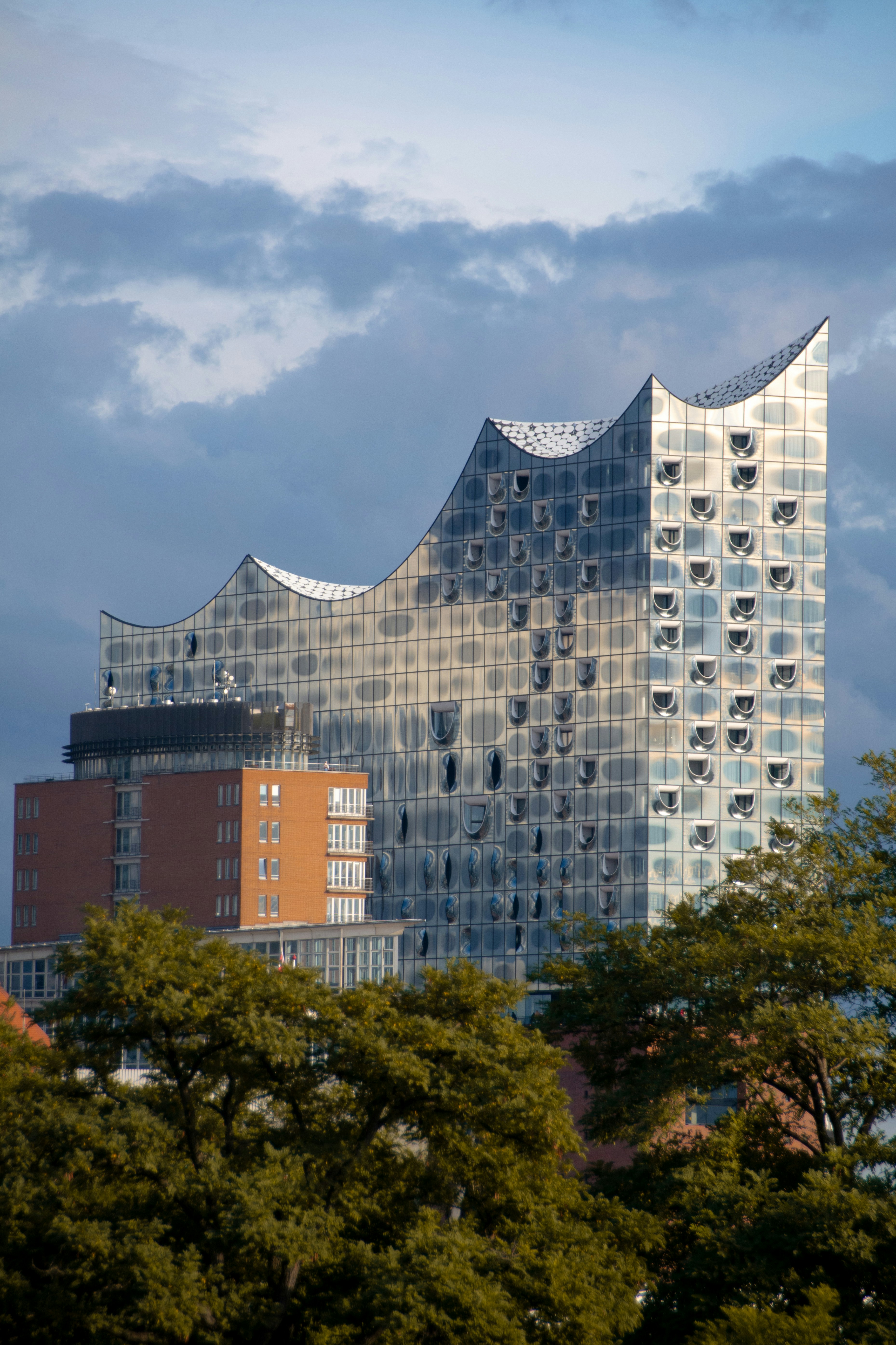 The modern "Elbphilharmonie" overshadowing a couple of trees at the port of Hamburg, Germany