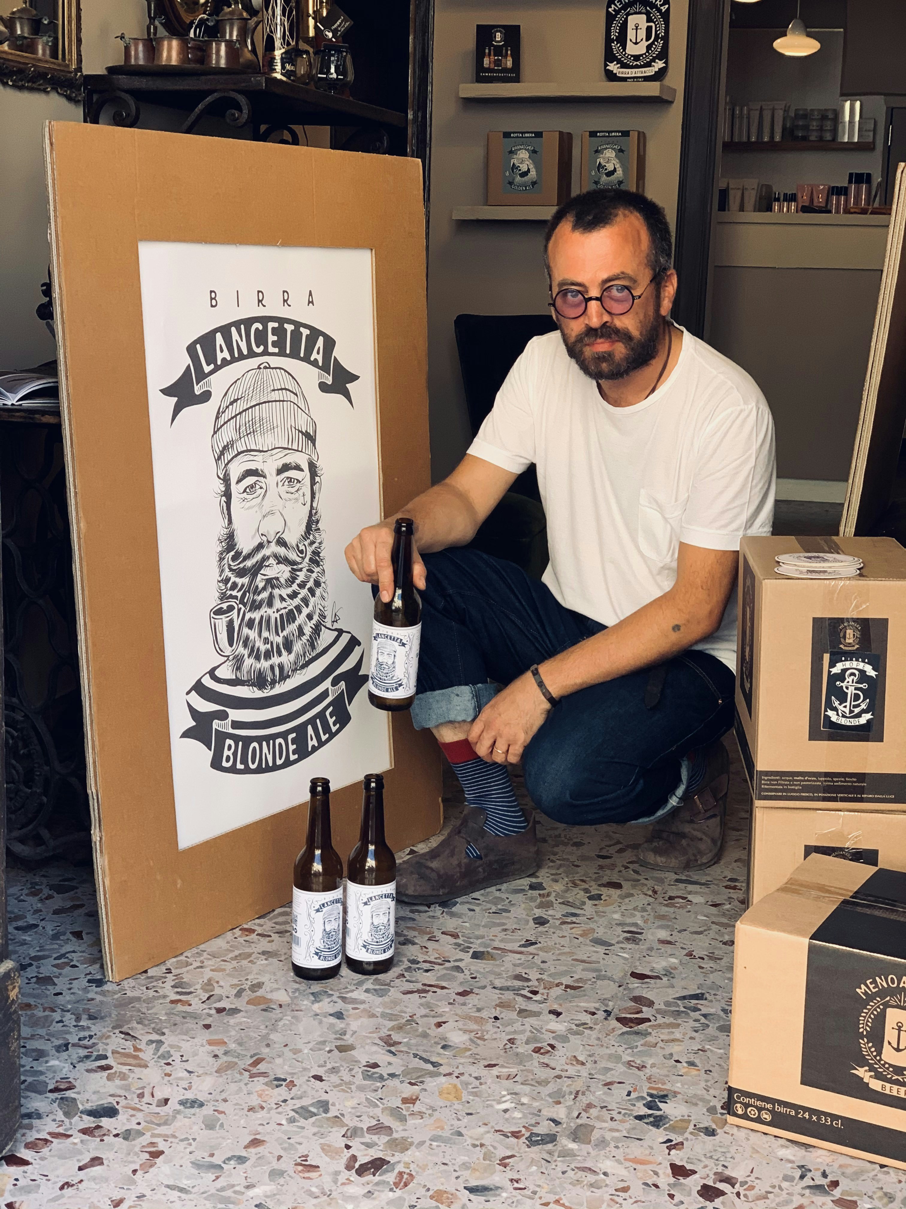 Man in a white shirt poses with Lancetta Blonde Ale bottles beside a prominent logo display. The setting reflects a creative brewing space.