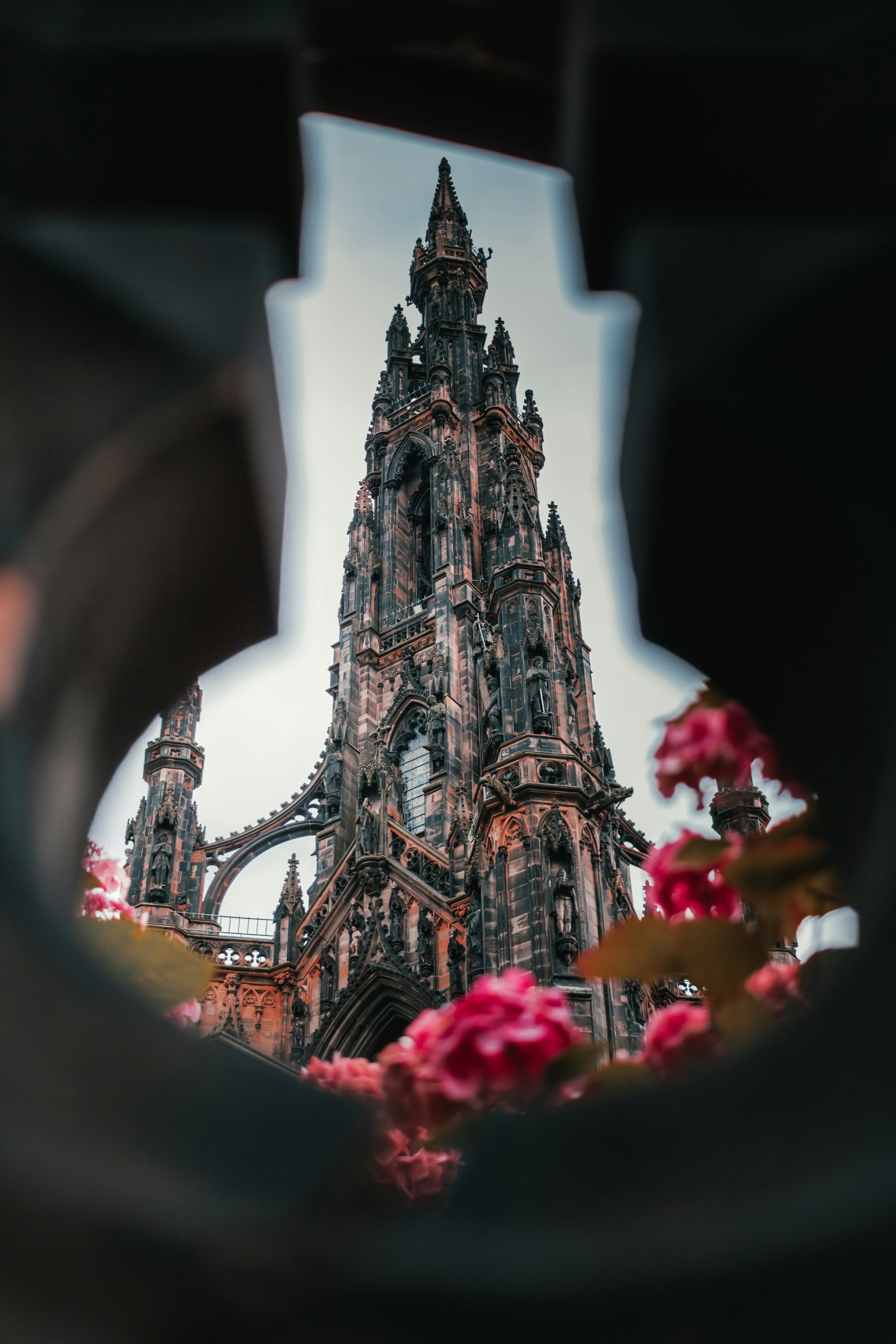 Gothic tower framed by vibrant flowers, showcasing intricate architectural details against a moody sky.