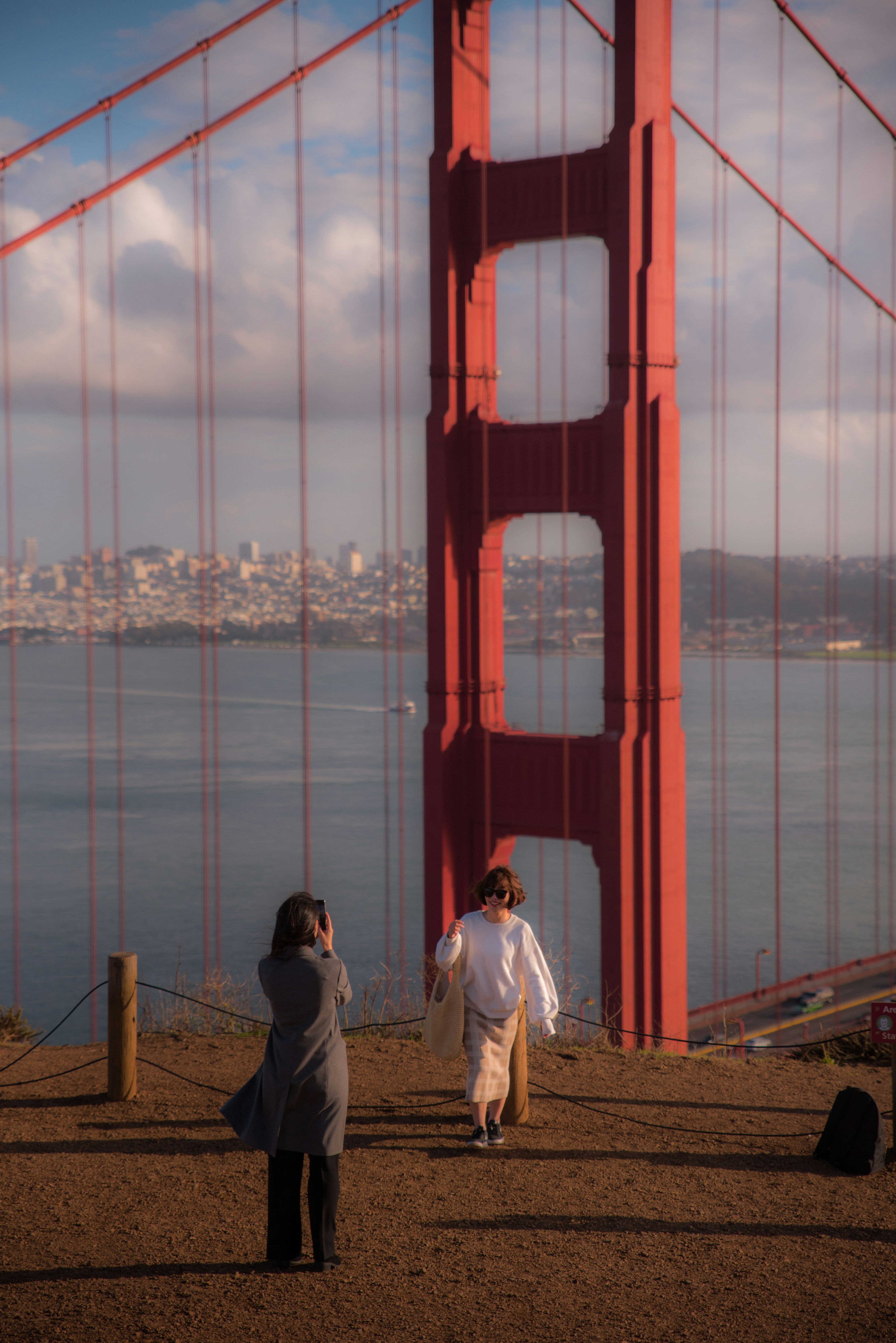 Two individuals pose for a photograph in front of the Golden Gate Bridge, showcasing the iconic structure against a backdrop of San Francisco's skyline.