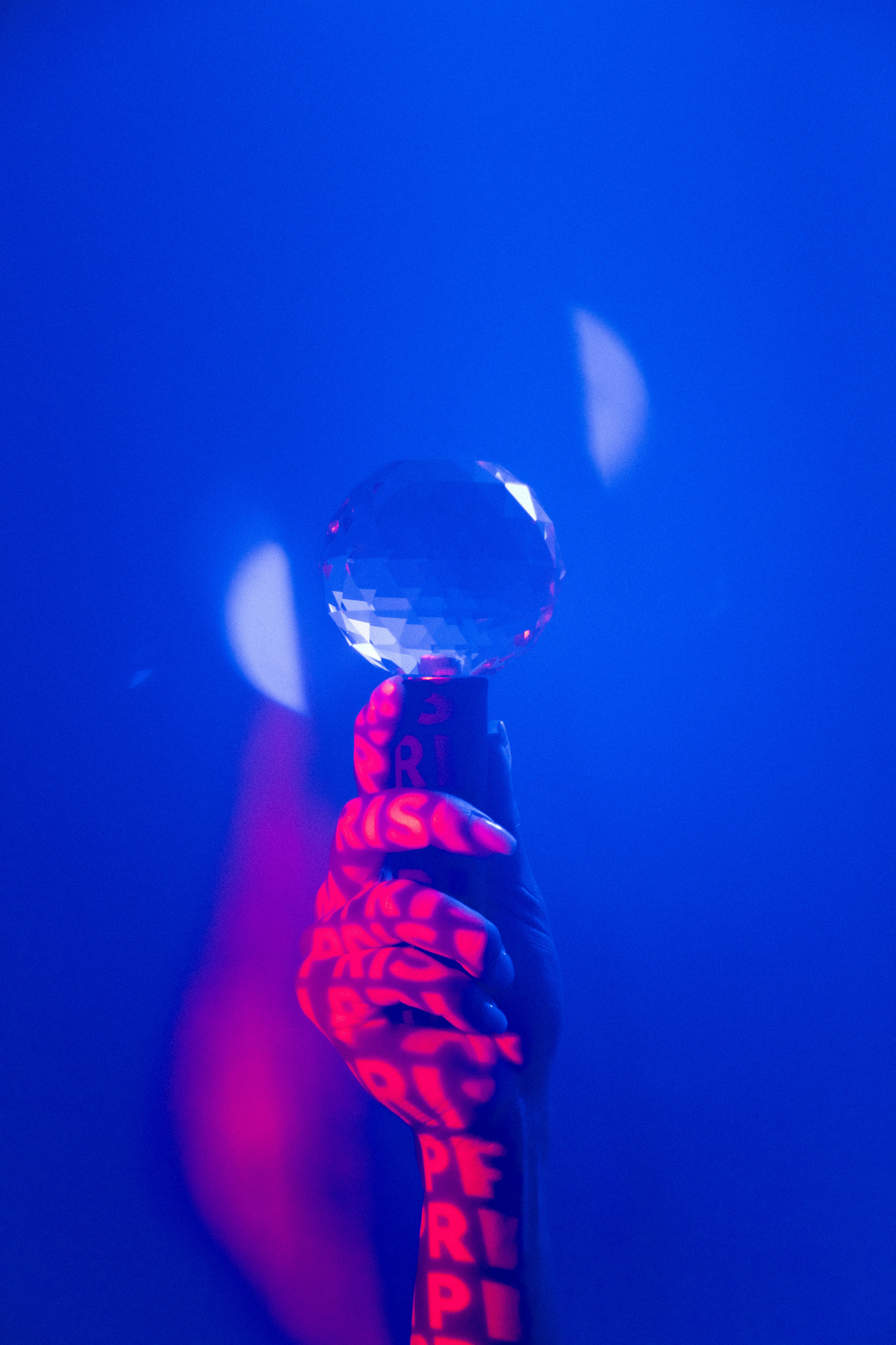 A hand holding a crystal ball, illuminated by vibrant blue and purple lights, casting intriguing patterns. The hand features projected text, enhancing the visual narrative.