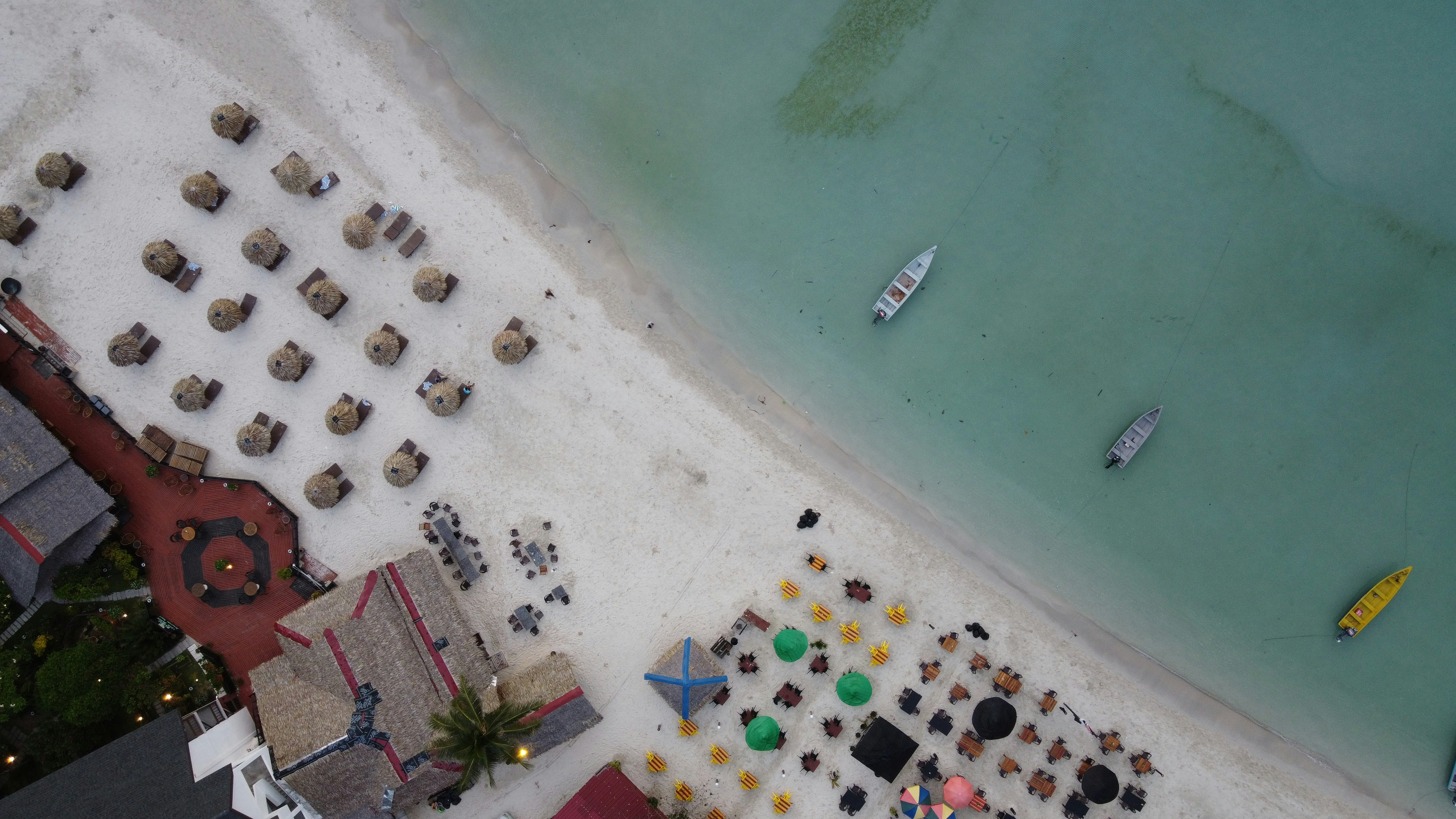 Aerial view of a beach with rows of tables and chairs beside turquoise waters.